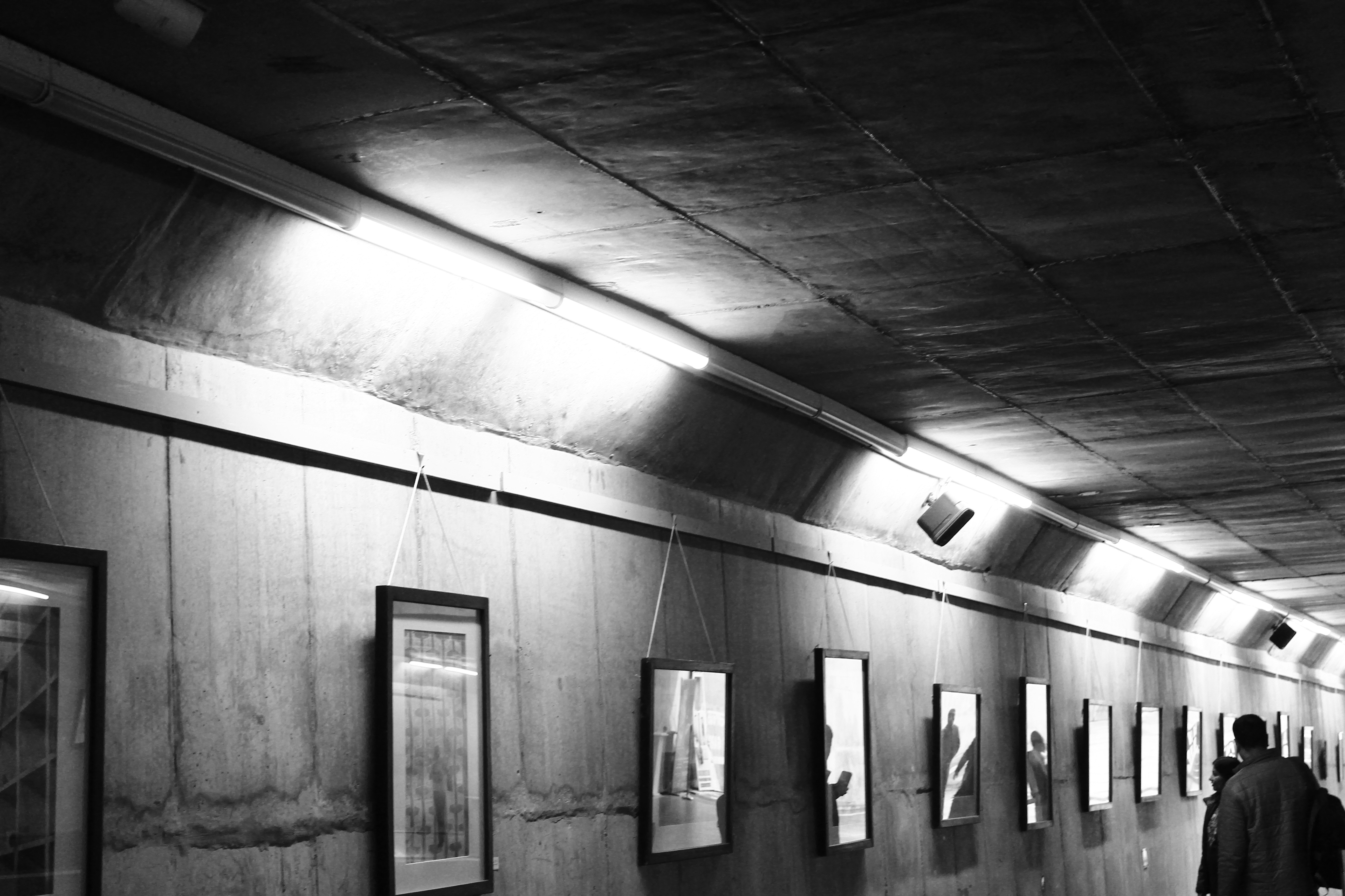 Black and white corridor with framed artwork lining the walls under bright ceiling lights.