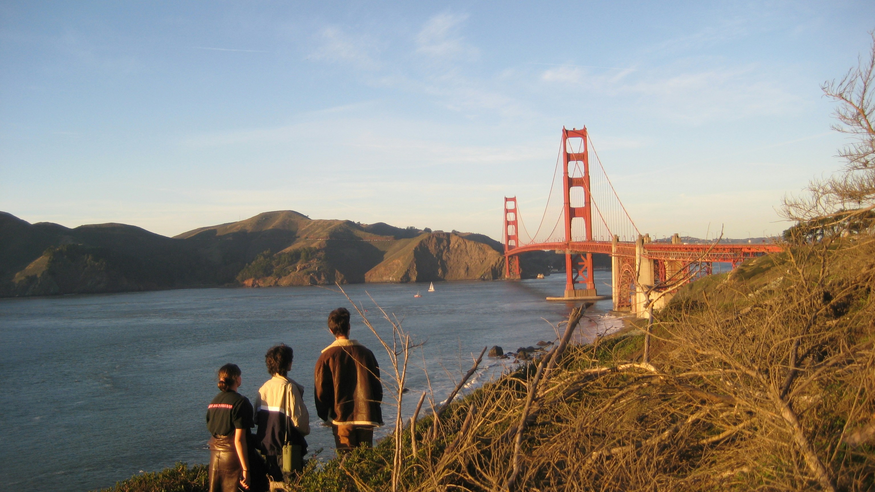 A trio of hikers gaze toward the Golden Gate from a windswept hillside