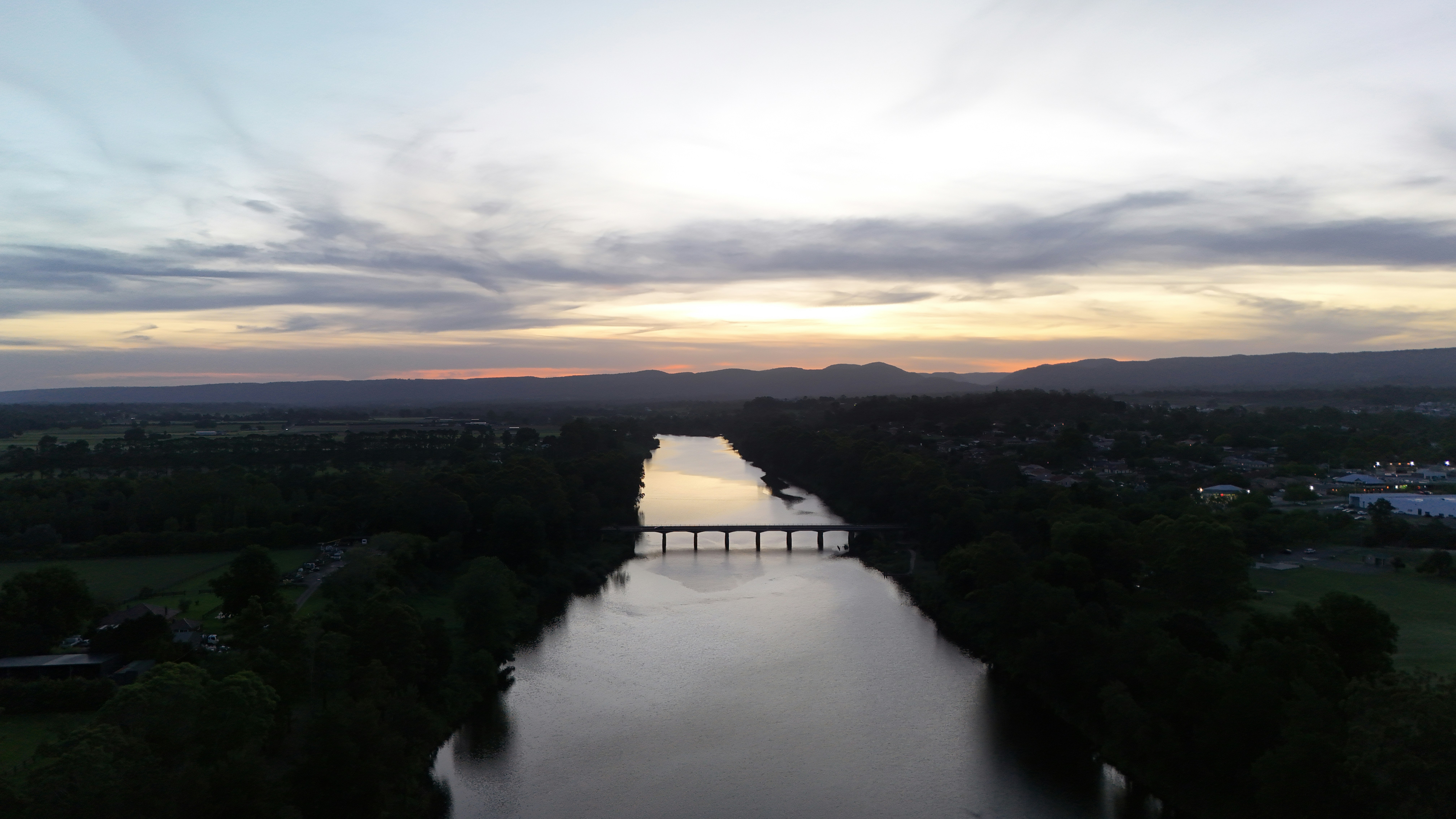 A serene river meandering through lush landscapes under a twilight sky, with a bridge elegantly spanning the water's surface.