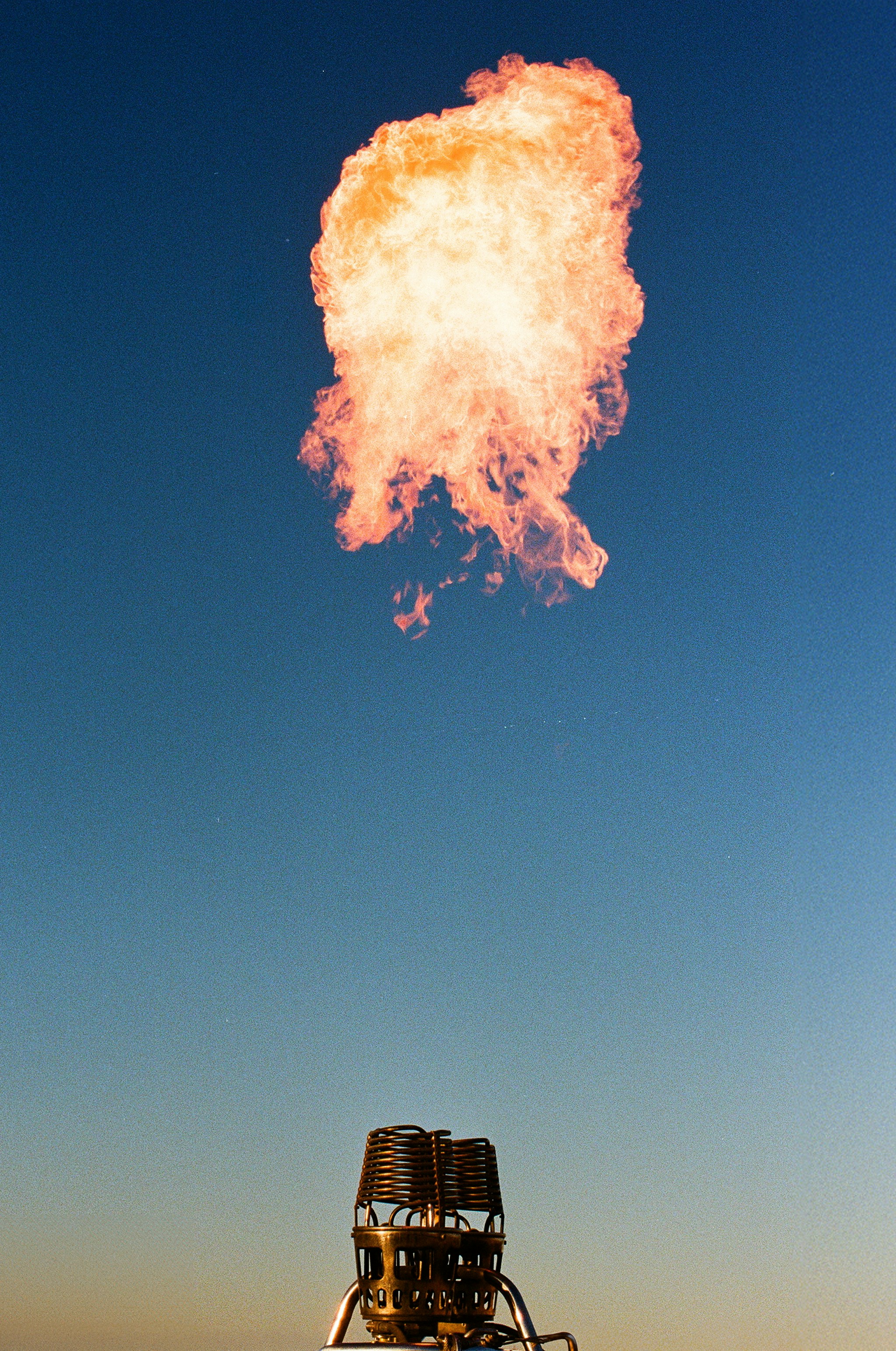 A pink-orange rocket plume erupts high in the clear dusk sky above a compact launch platform, capturing a dramatic test moment.