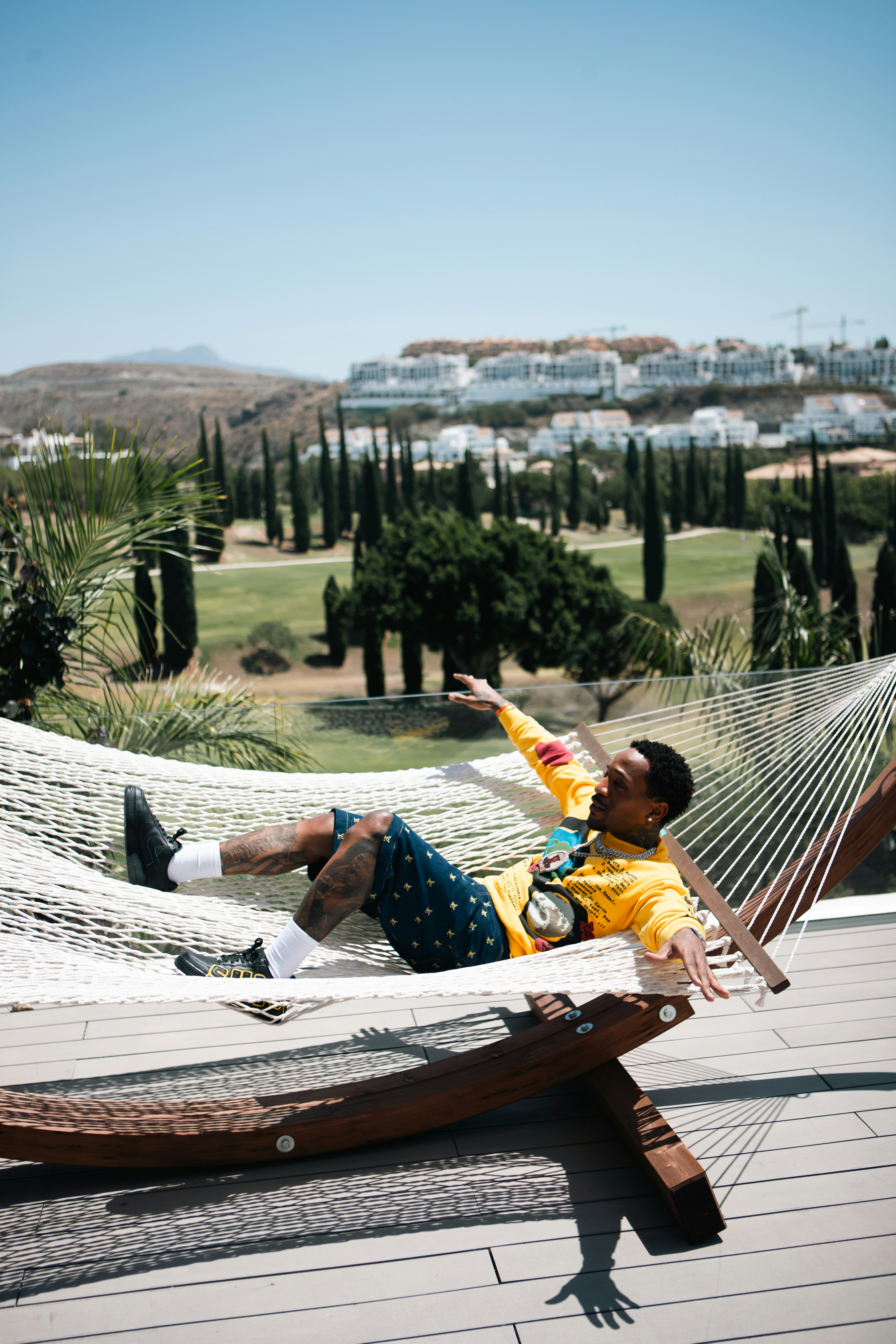 Person relaxing on a hammock overlooking a sunny landscape with distant hills and trees.