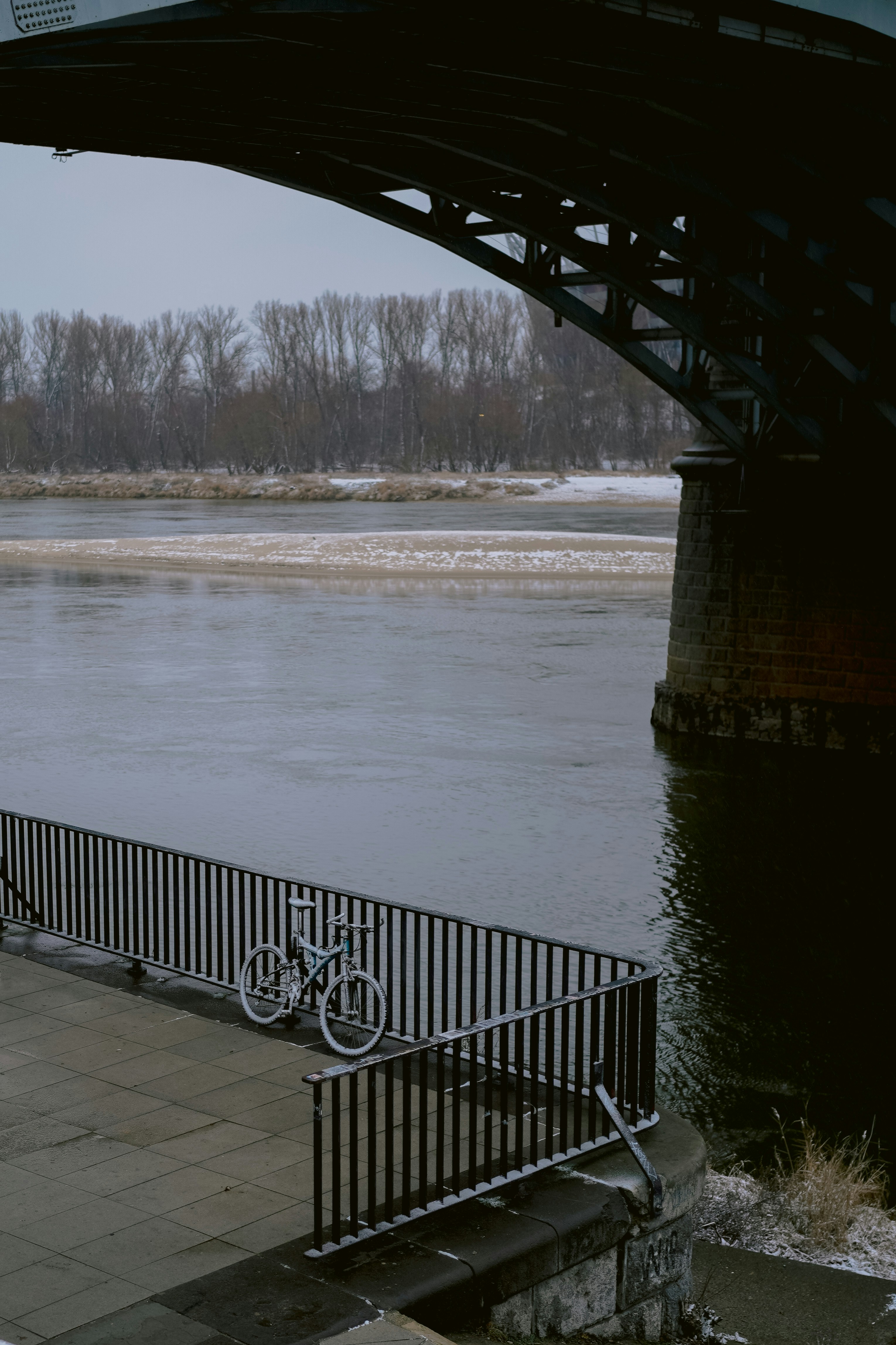 White Bicycle by the Riverbank Beneath the Iron Bridge in Winter Light