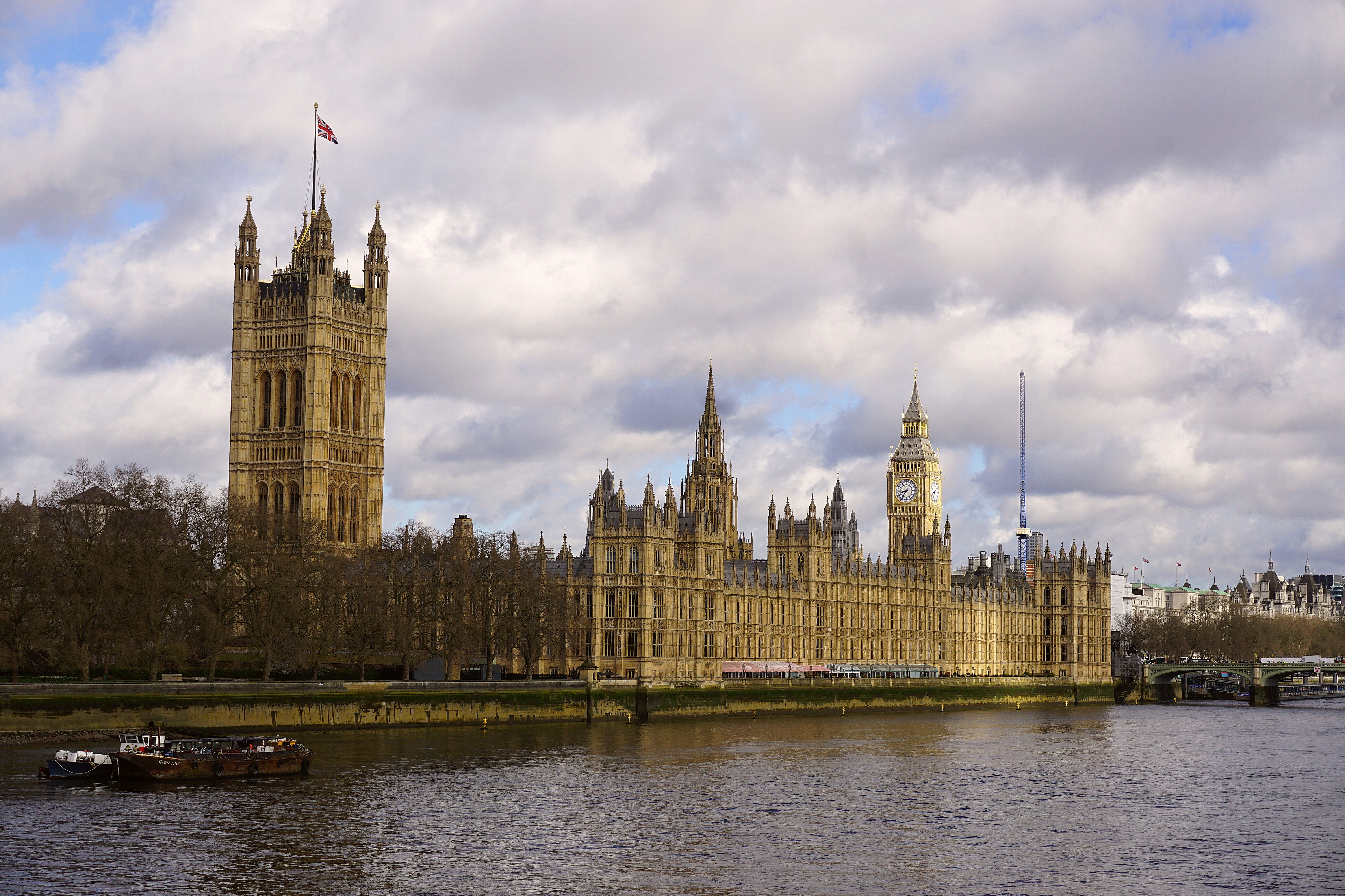 Gothic-style palace with tall towers beside a wide river under a partly cloudy sky.