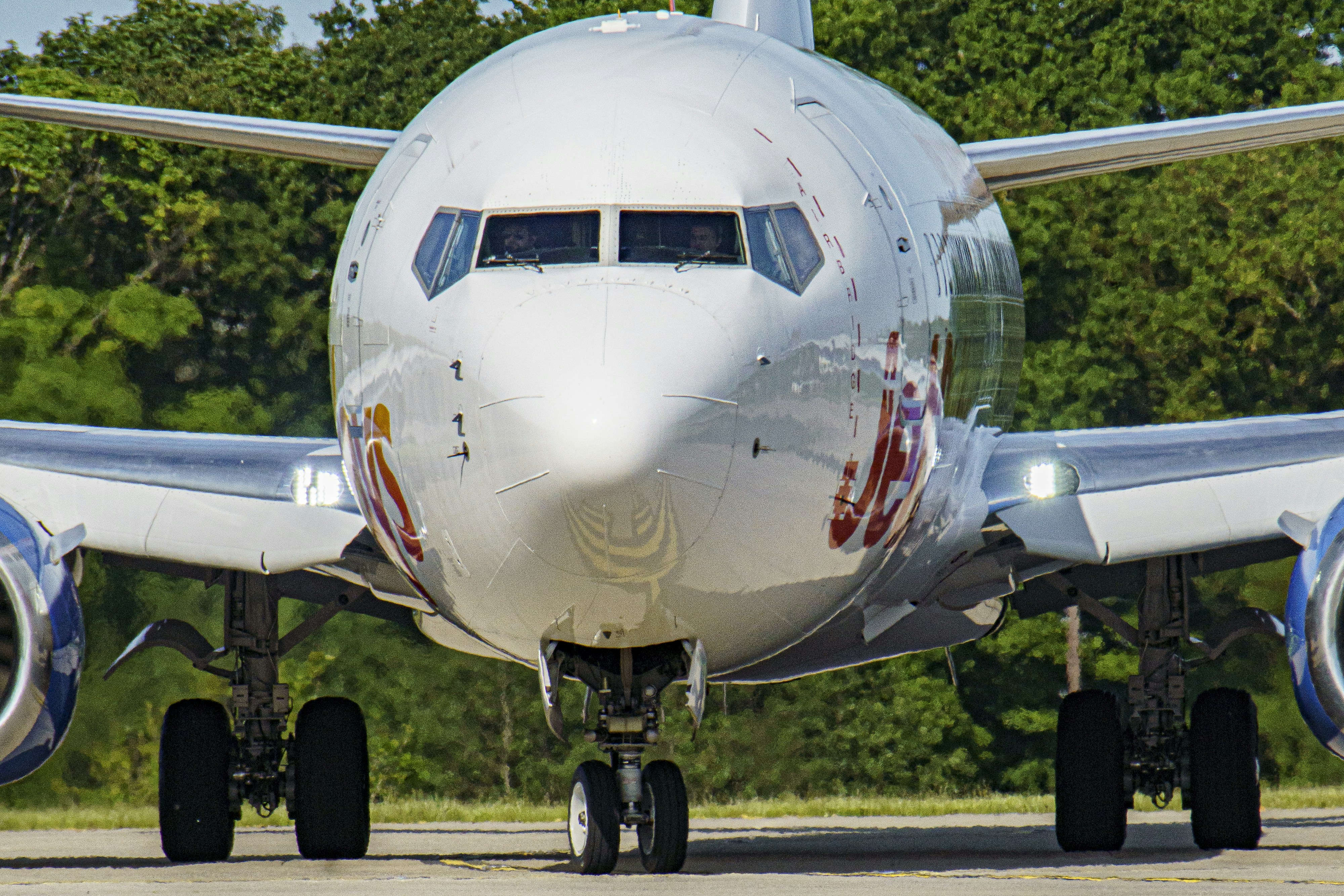 Commercial airplane taxiing on runway with lush green backdrop and sunlight highlighting its sleek design.