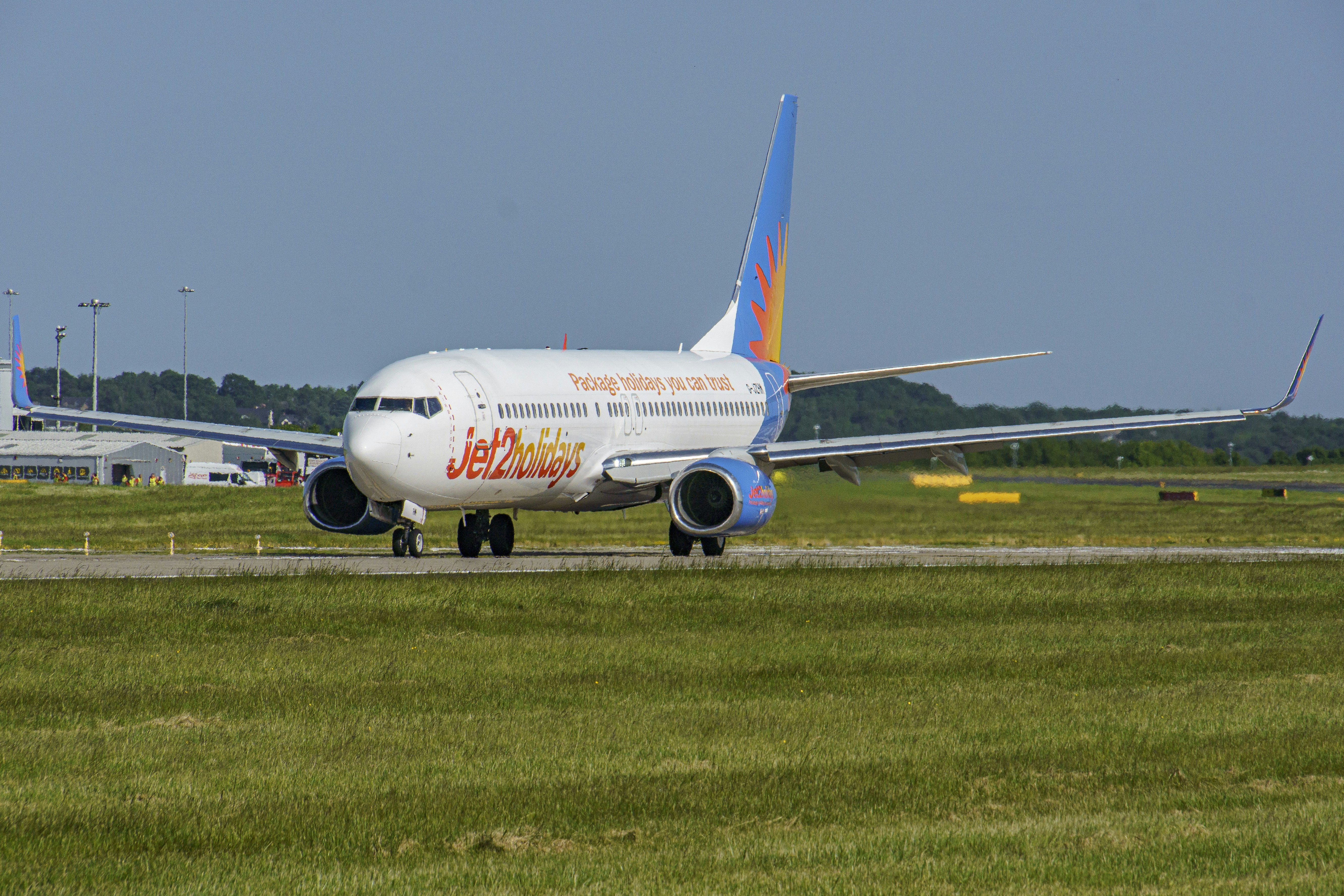 Jet2 Holidays aircraft taxiing on a runway with vibrant livery against a clear blue sky and lush green grass.