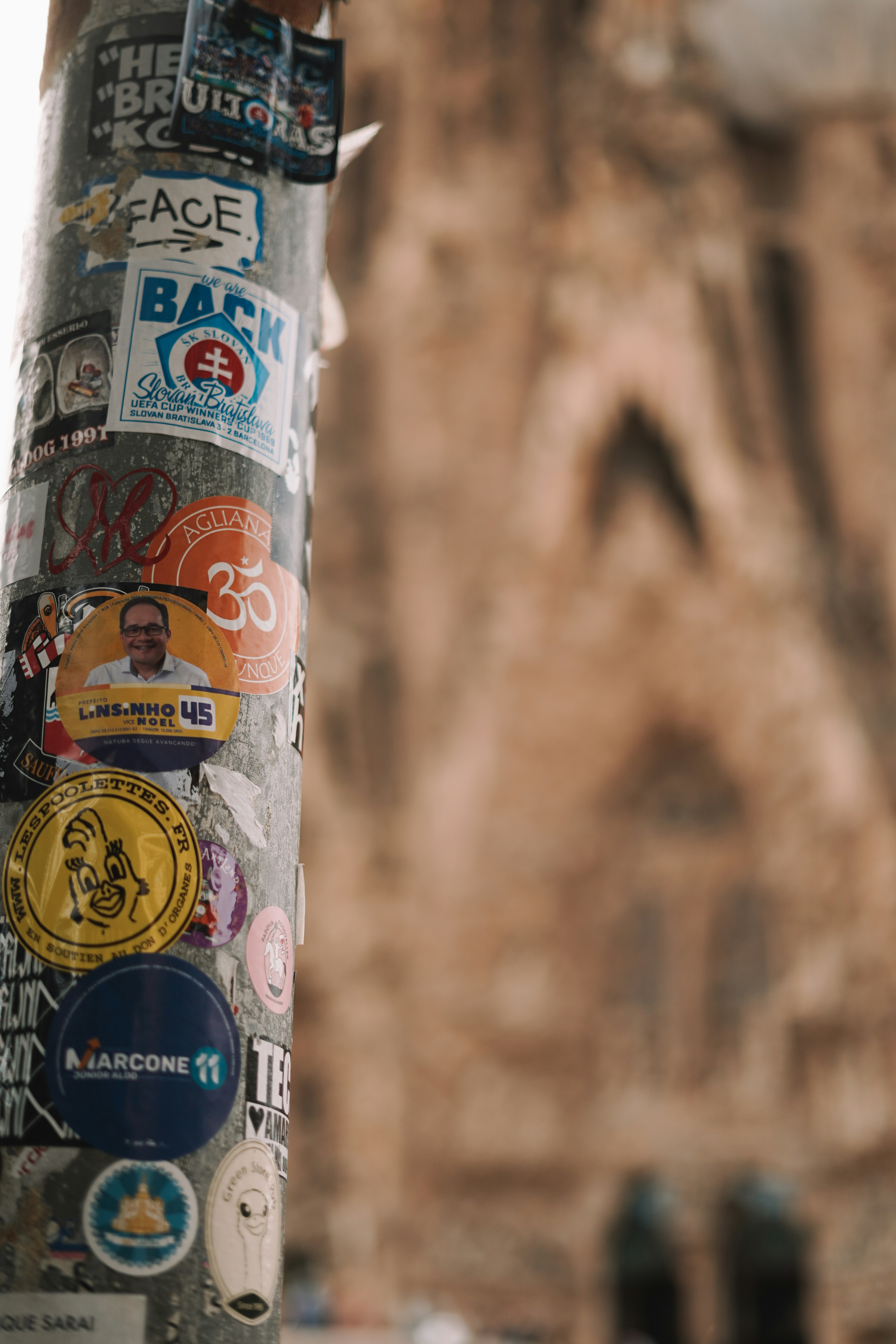 Sticker Mosaic on a Street Pole: A Close-Up of Urban Labels Against a Blurred Brick Backdrop