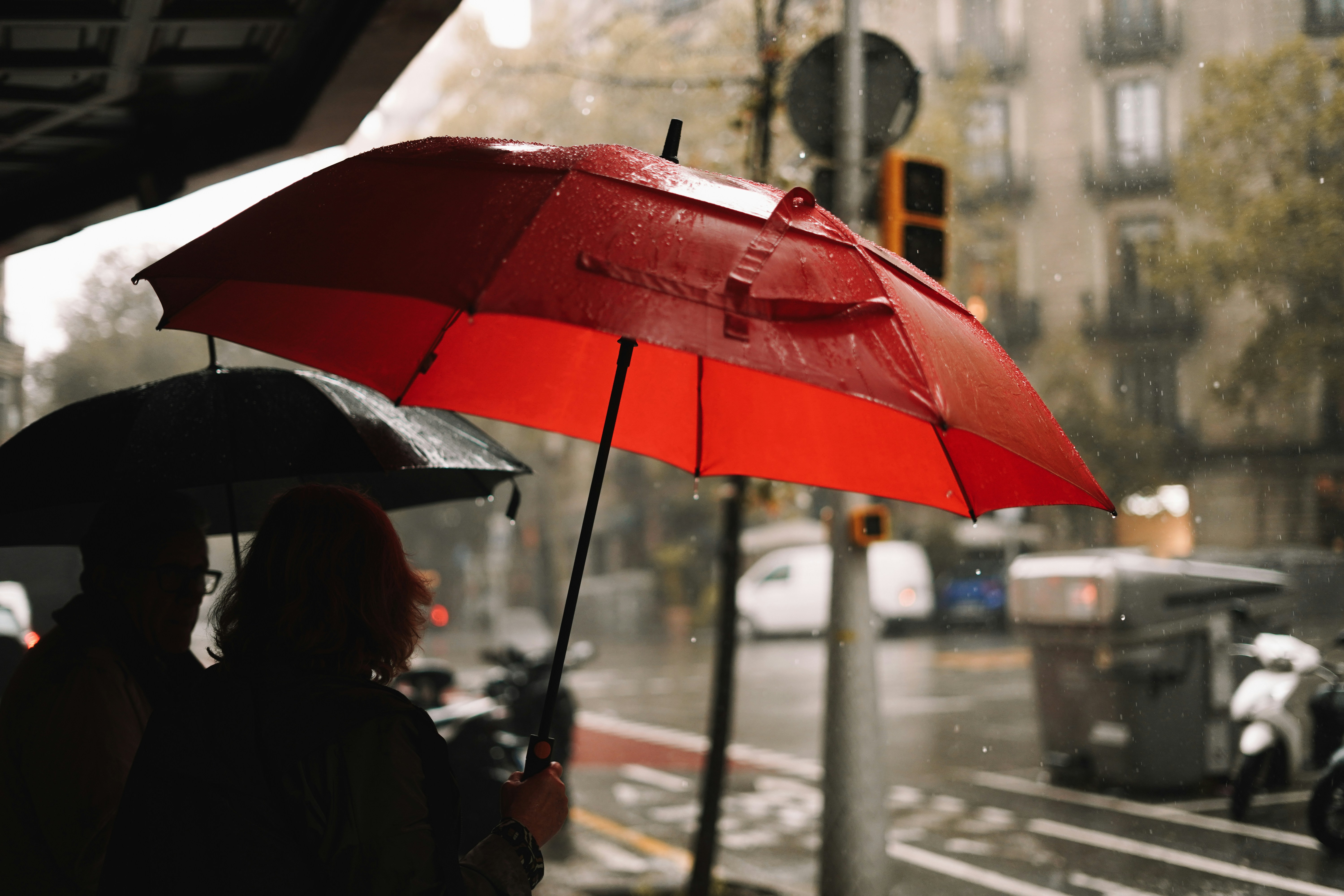 Woman with red umbrella and a man with black umbrella are waiting to rain be over
