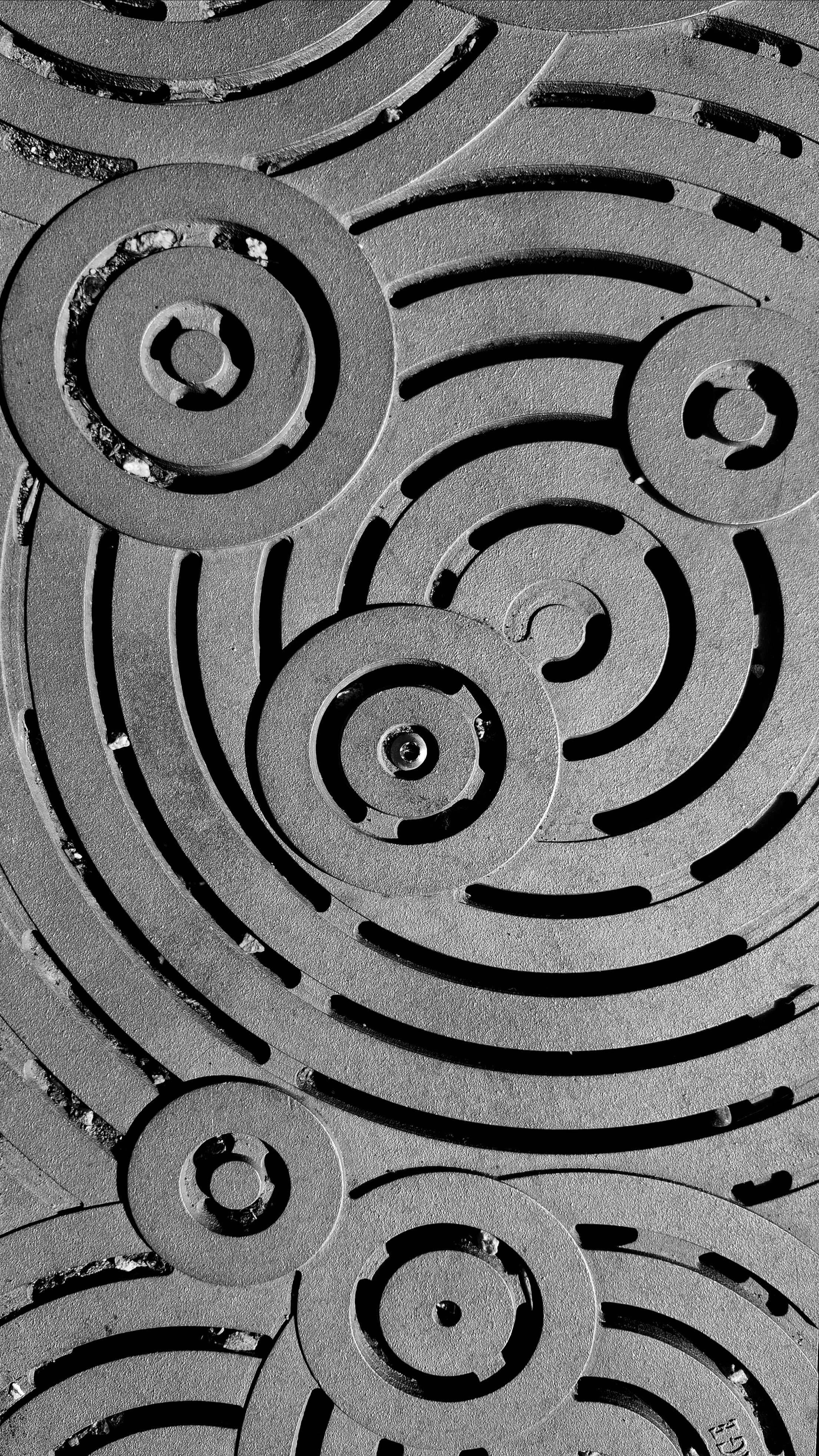 Close-up photograph of a grayscale metal grate with interlocking circular discs and bolts.