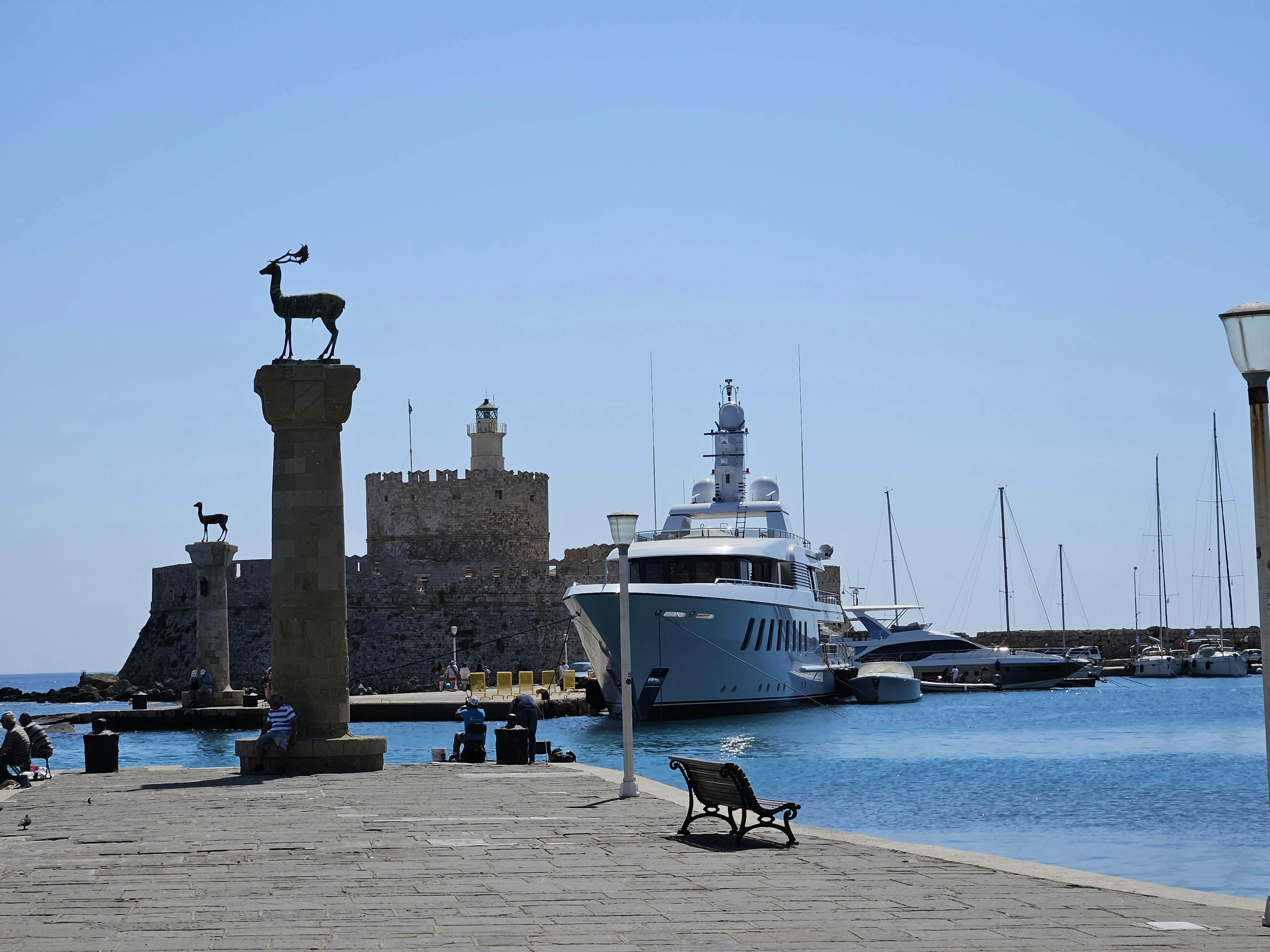 Column Sentinel by the Marina: A Stone Bird Statue Over Calm Waters and Yachts