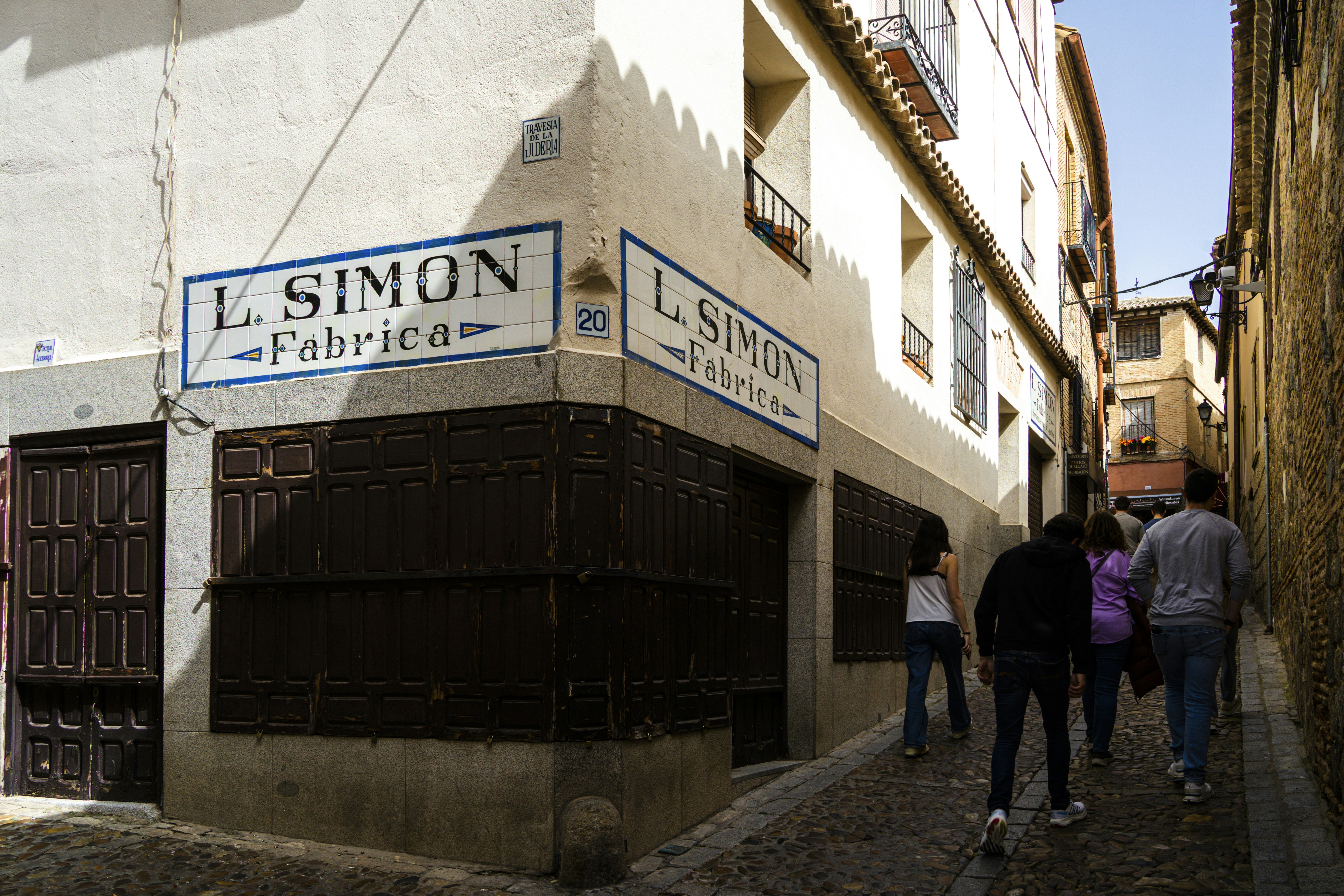 People walking through a narrow alley with sunlight casting shadows on the textured walls.