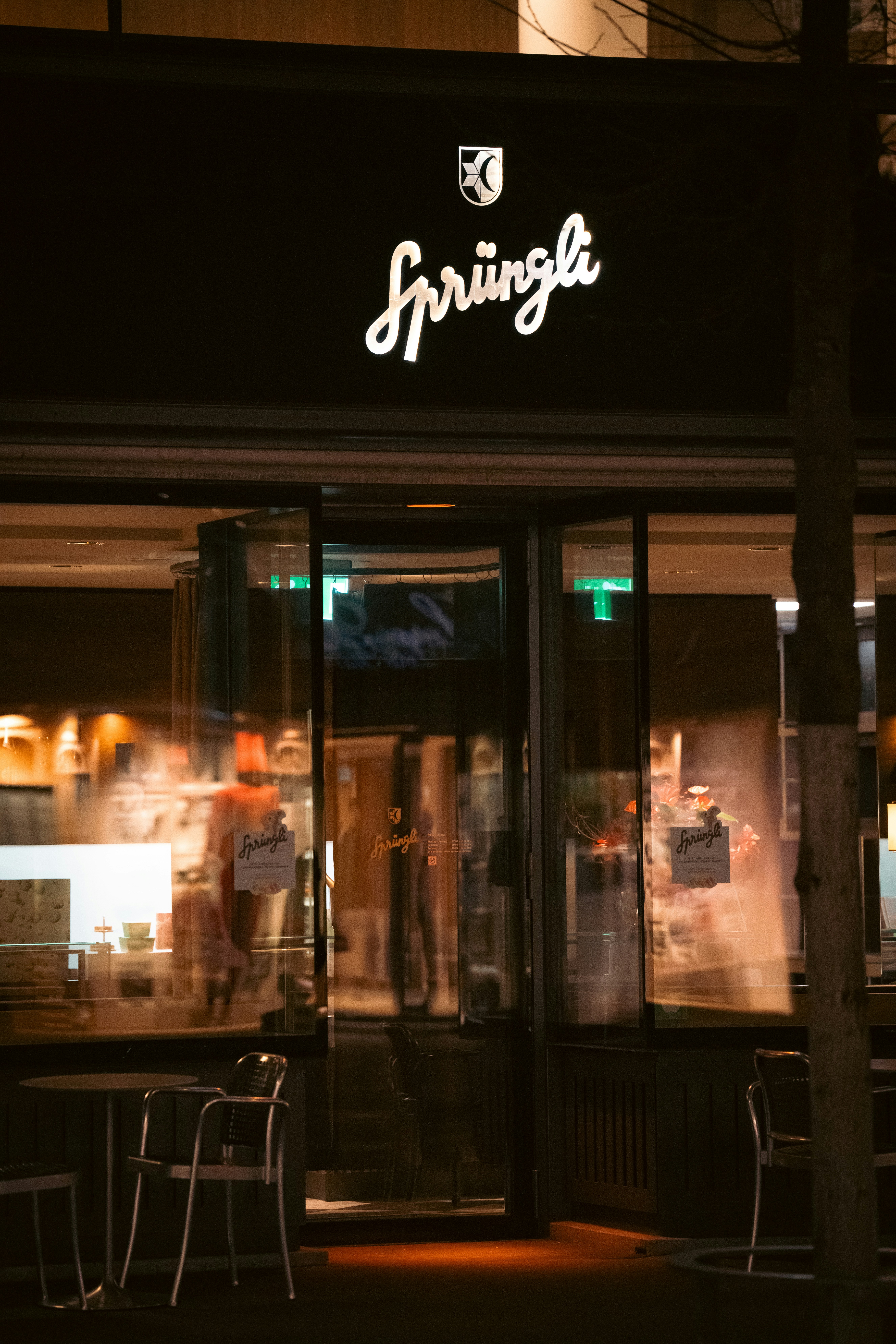Night-lit Sprüngli storefront: warm interior glow through glass