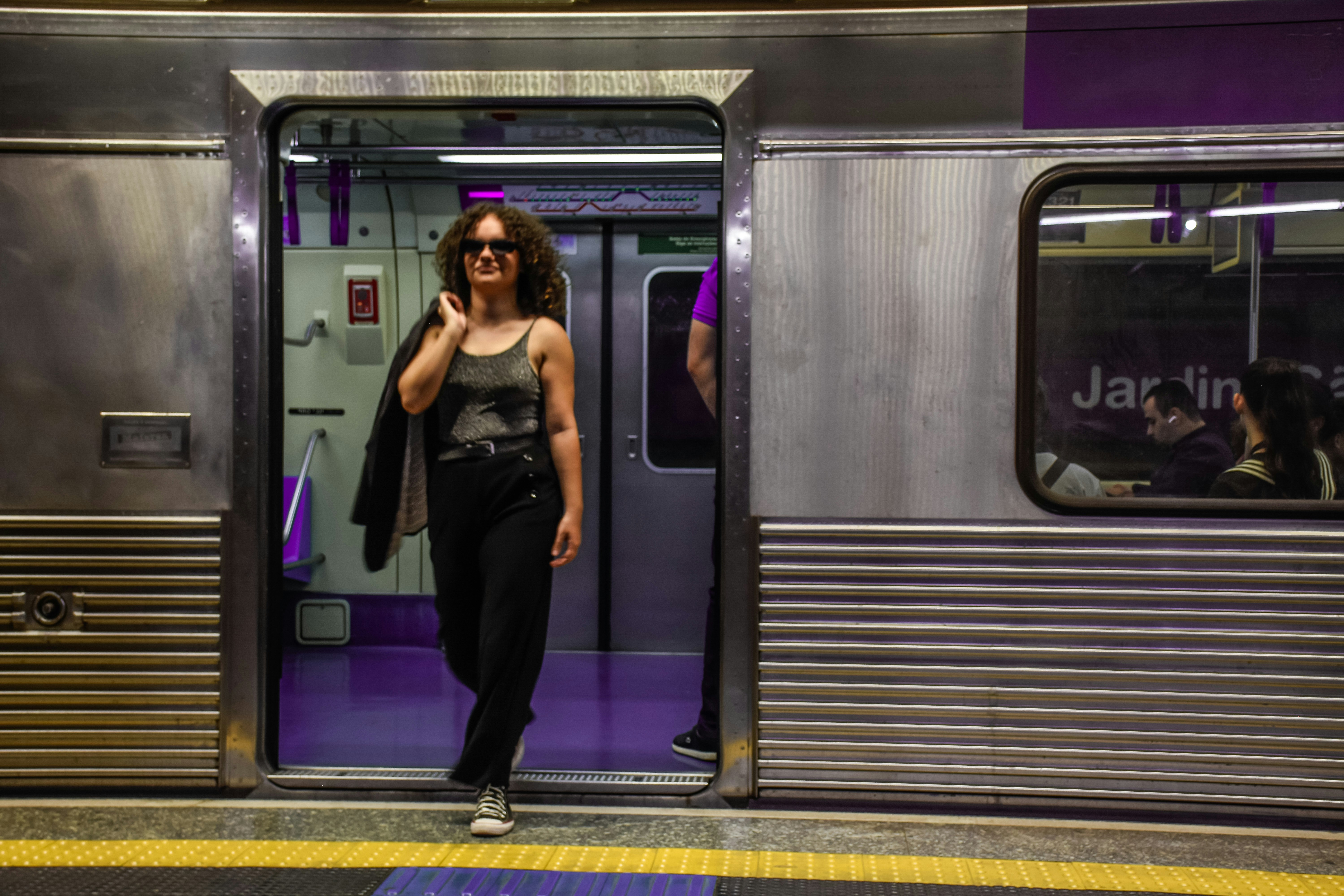 Person confidently stepping off a subway train with a metallic exterior, contrasting against the vibrant purple interior.