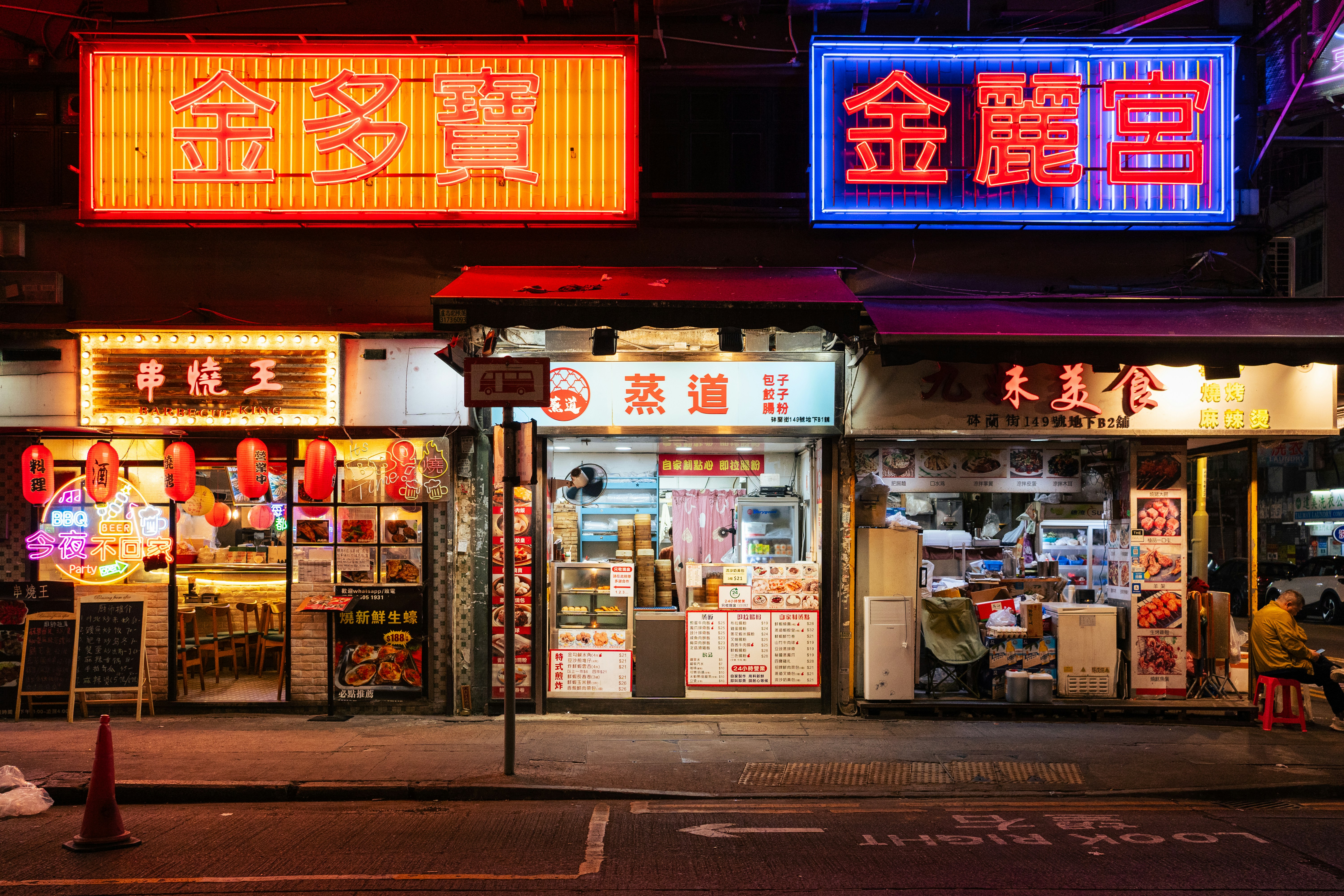 Colorful neon signs illuminate a row of bustling shops at night.