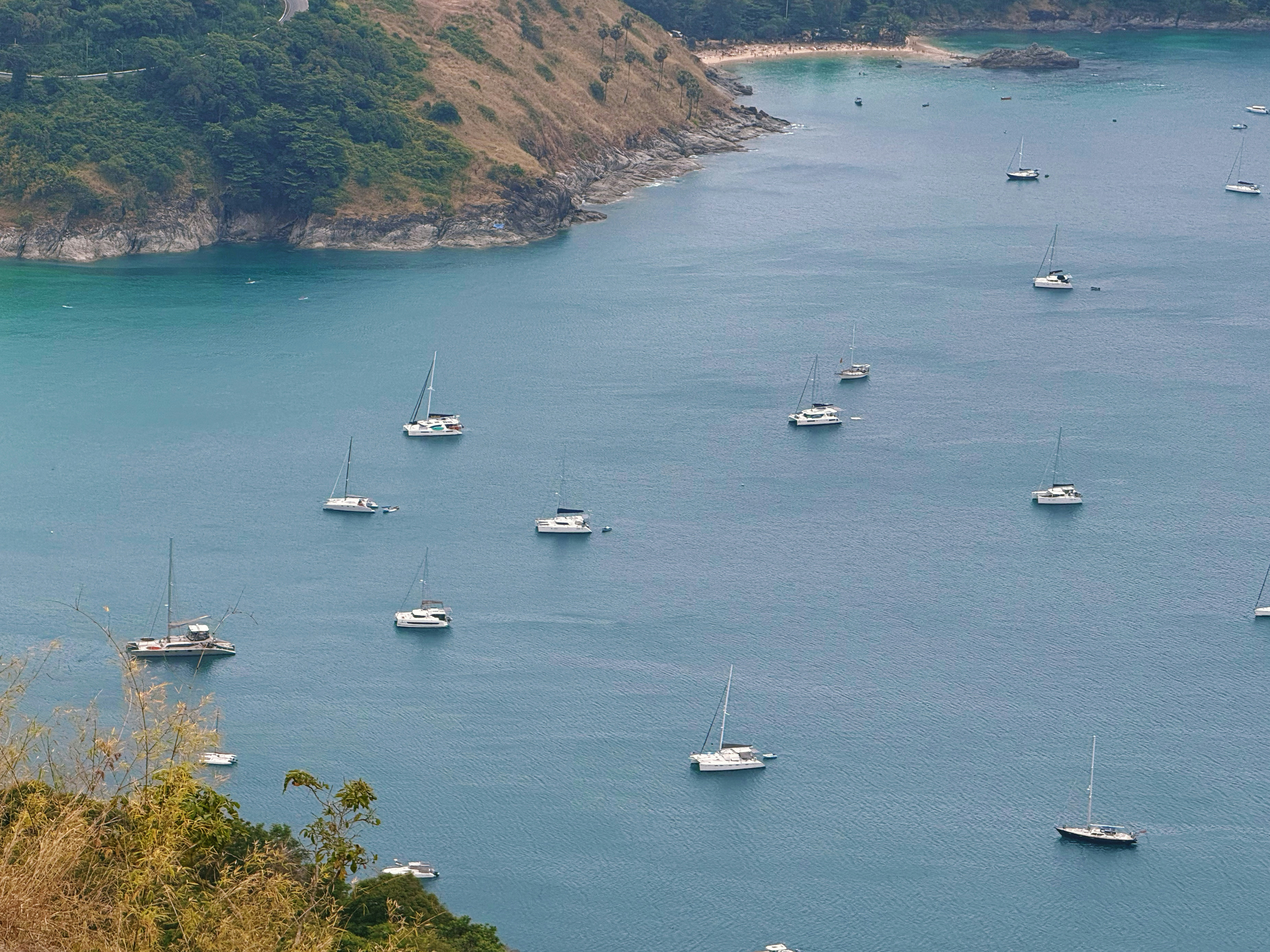 Sailboats scattered across calm turquoise waters near a rugged coastline.
