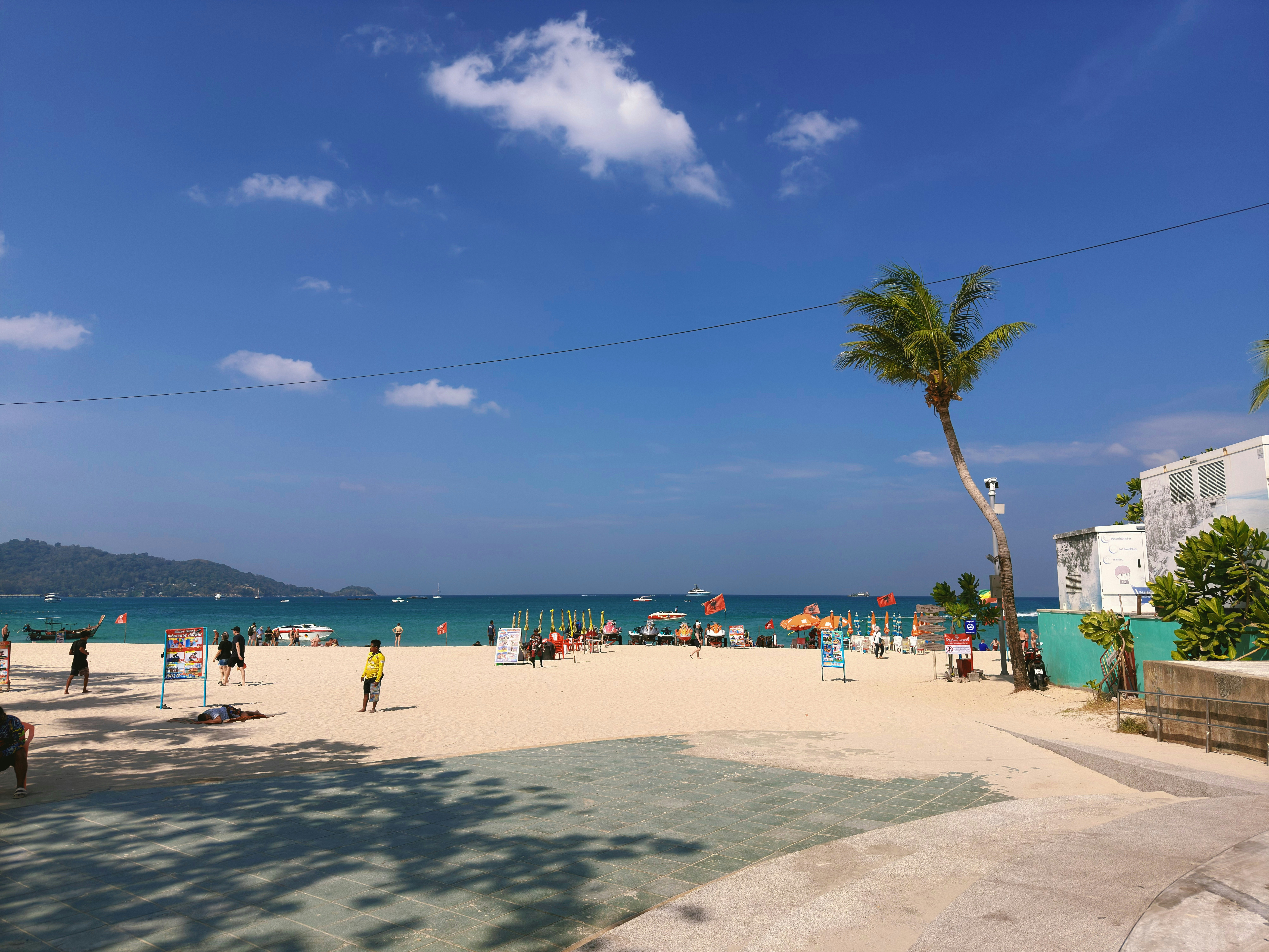 Sandy beach with sunbathers and palm trees under a clear blue sky.