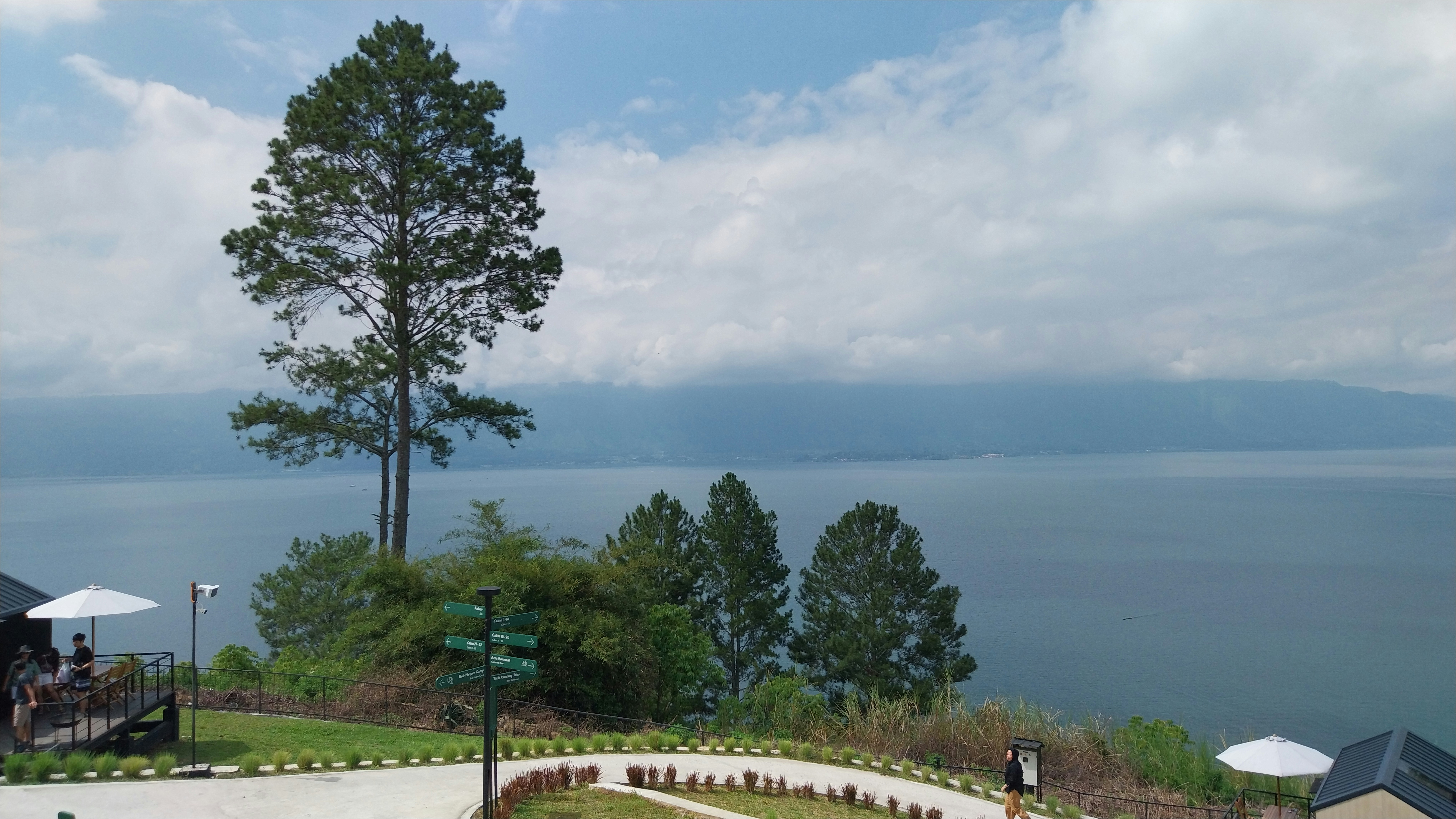 Lush greenery and trees overlooking a tranquil lake under a partly cloudy sky.