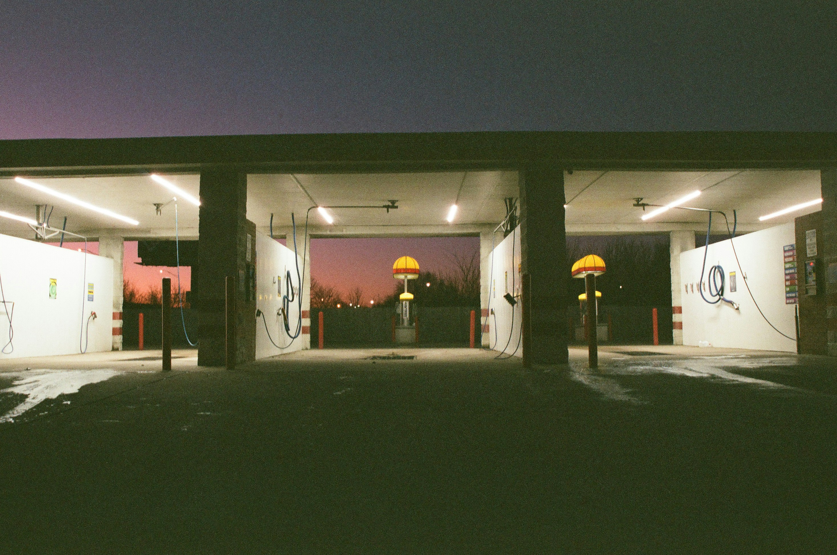 Empty car wash bays under a dusky sky with distant trees silhouetted.