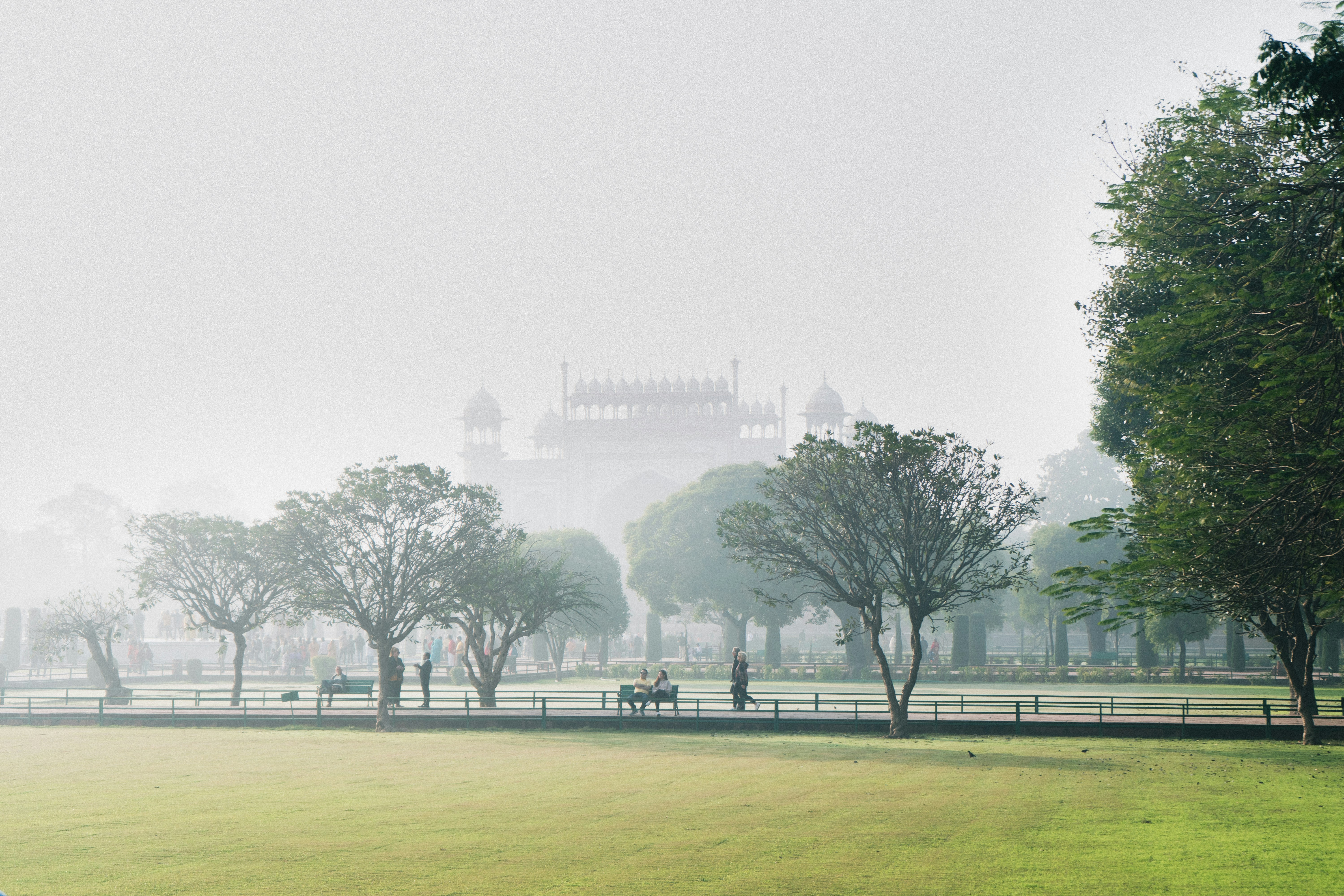 Silhouette of a grand structure in a misty garden with lush lawns and scattered trees.