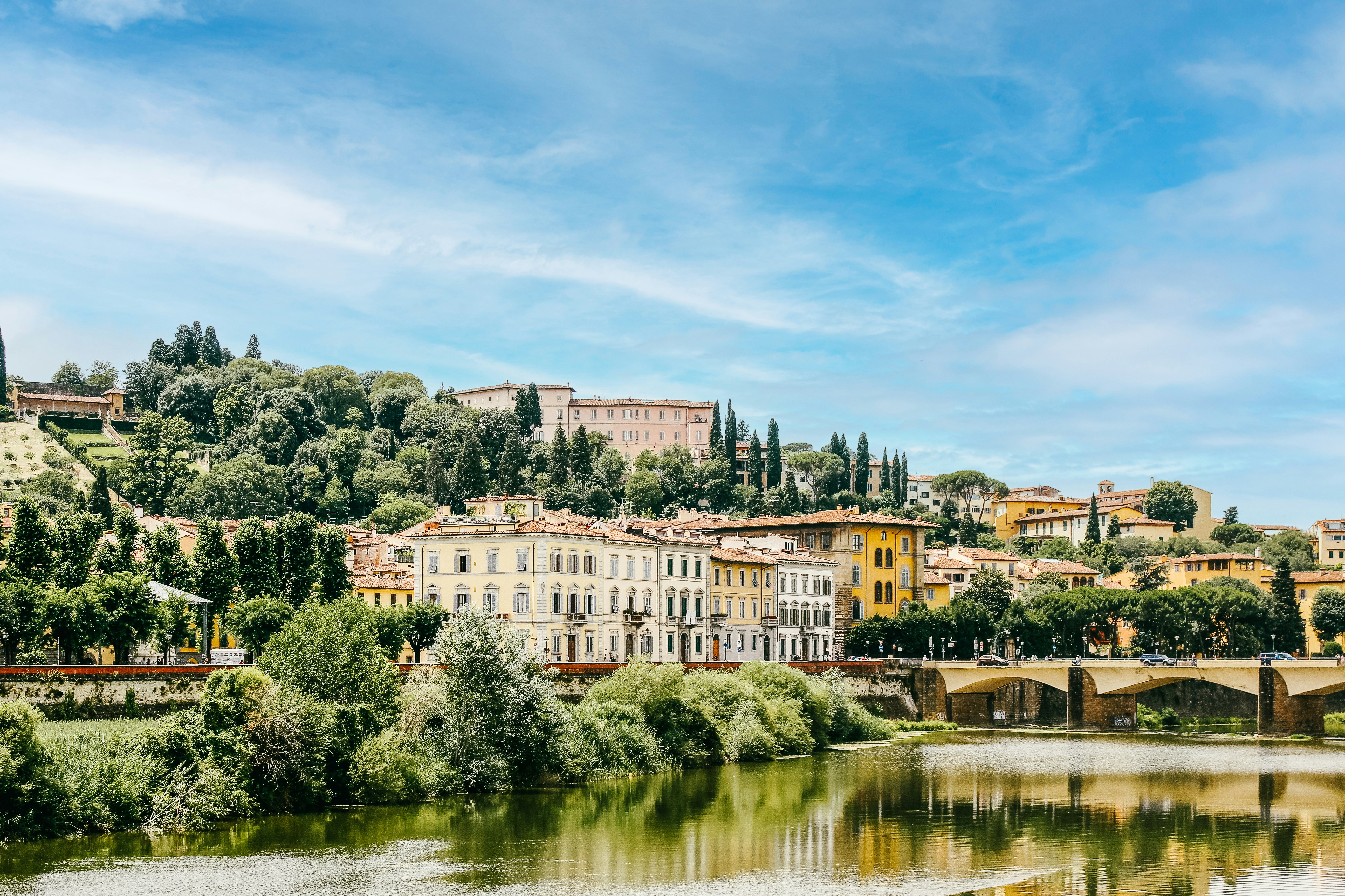 Historic Ponte alle Grazie spanning the Arno River, framed by lush greenery and classic Tuscan architecture under a vibrant sky.