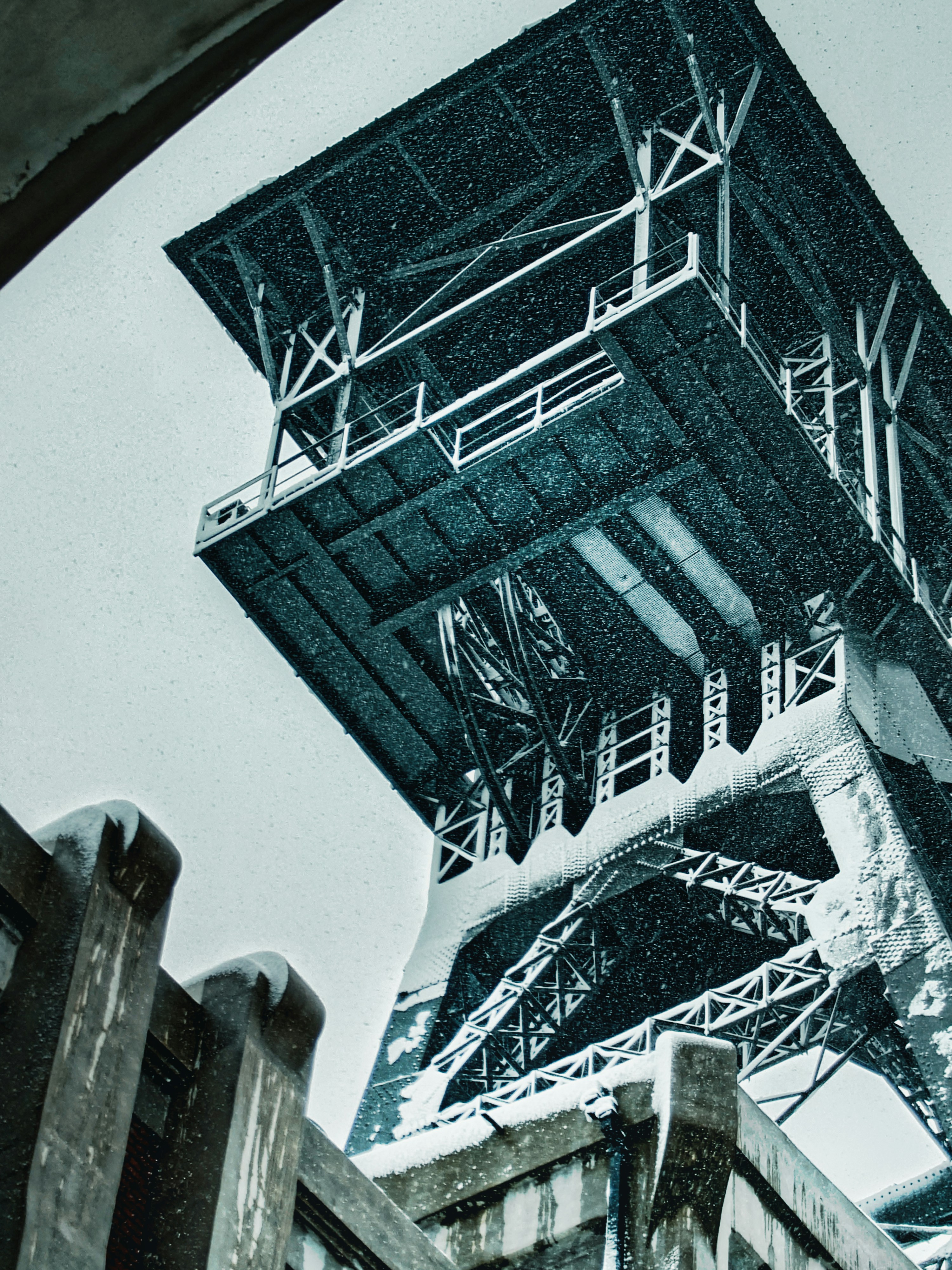 Snow-covered industrial tower seen from below against a gray sky.