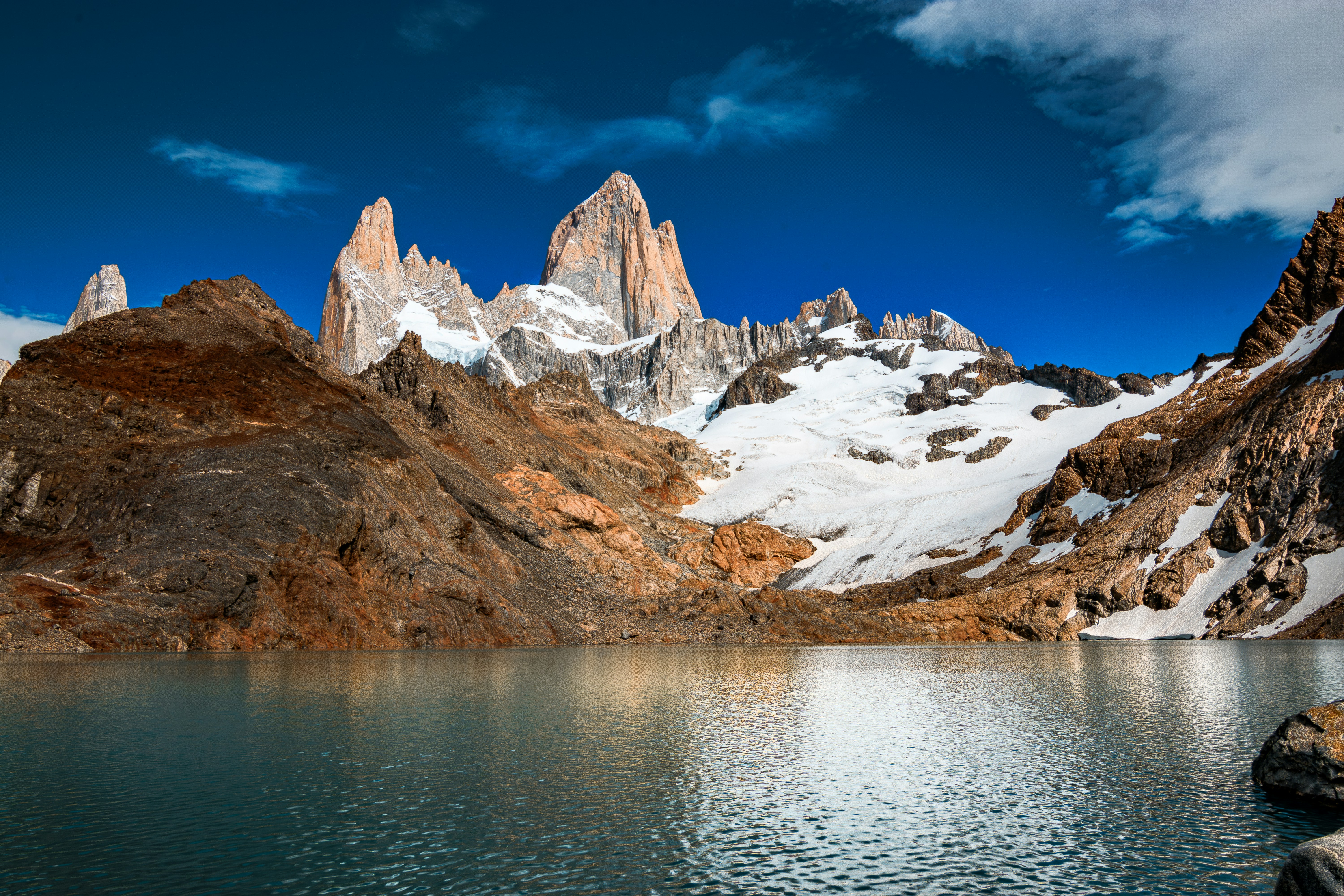 Snow-capped mountains reflected in a serene lake under a vibrant blue sky.