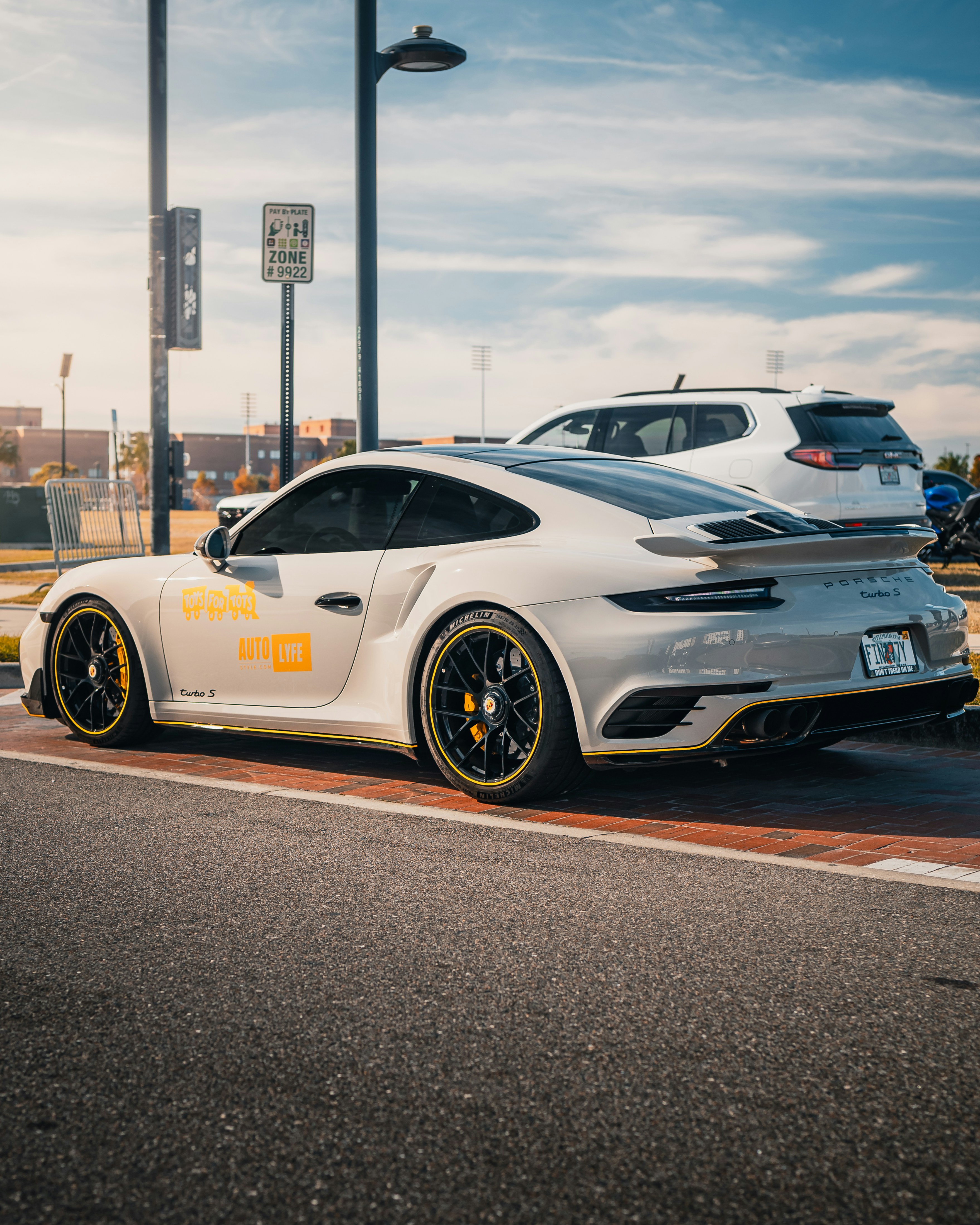 Sunlit White Porsche 911 with Bold Yellow Accents in a Modern Parking Lot