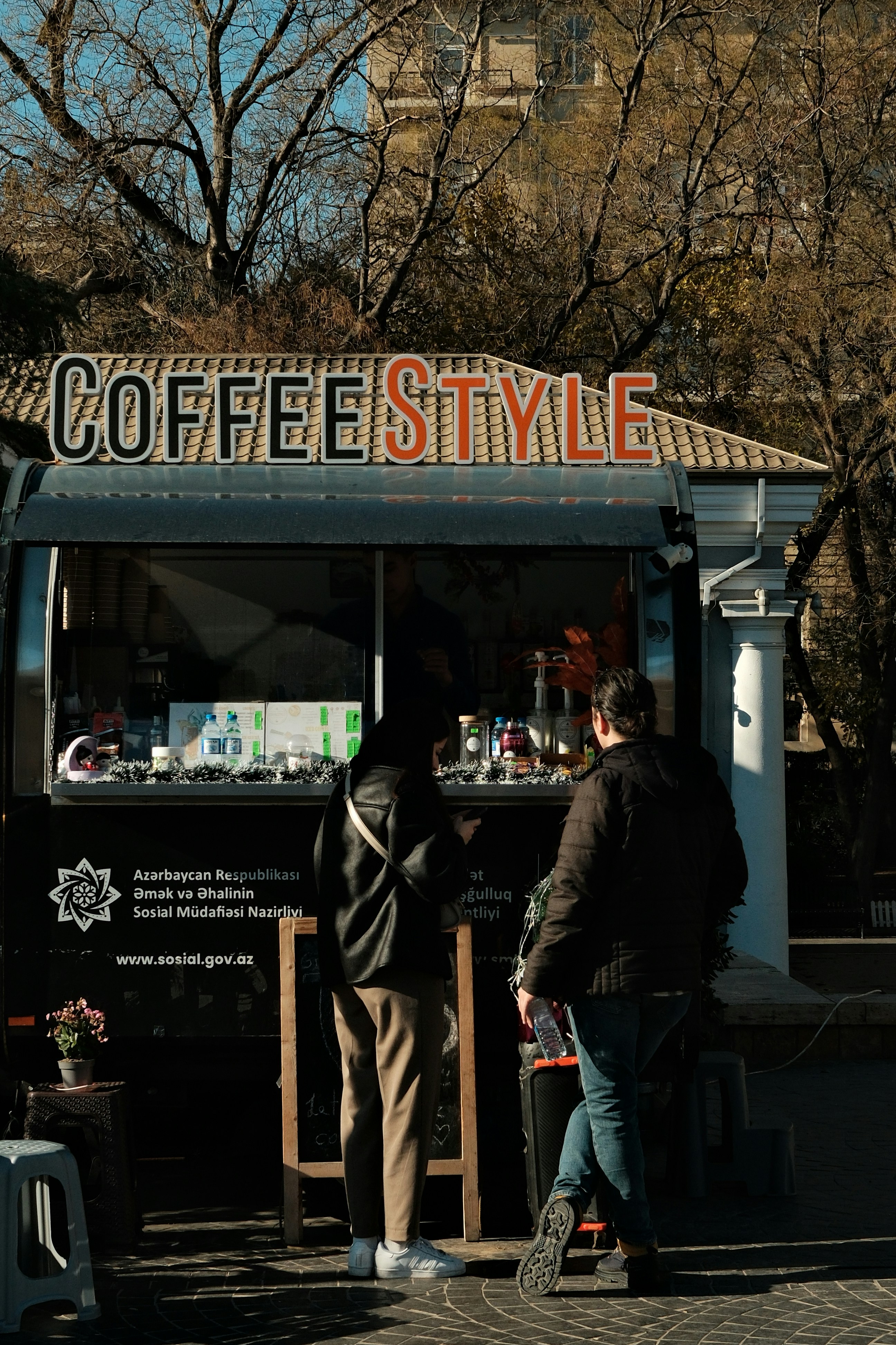 A couple of people standing outside of a coffee stand photo – Free ...