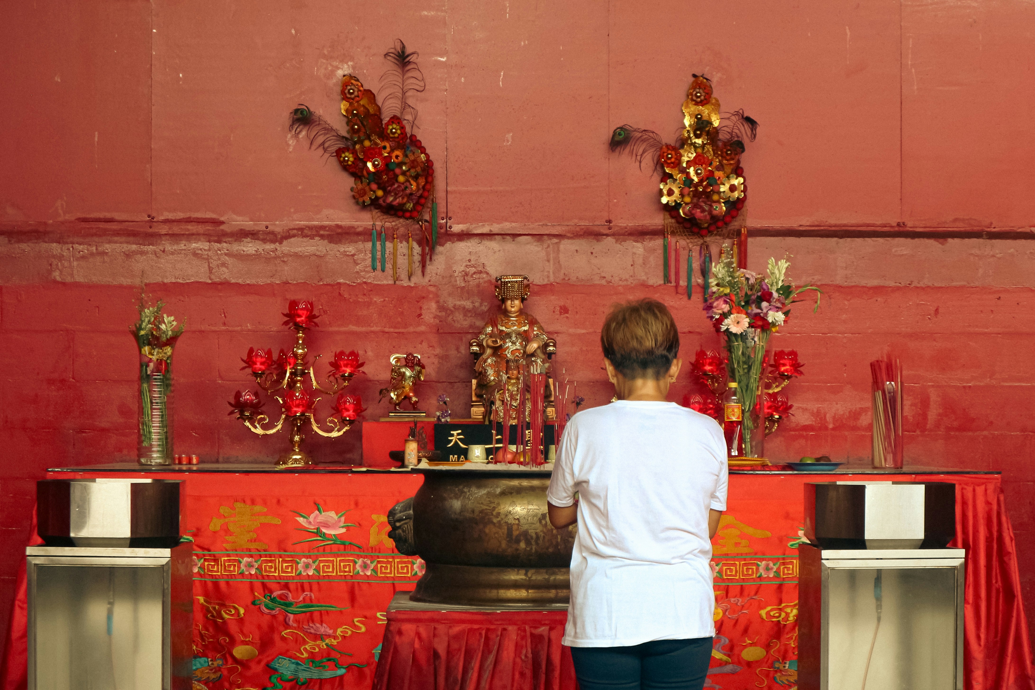 Person in white shirt stands before a richly decorated altar with red and gold accents.