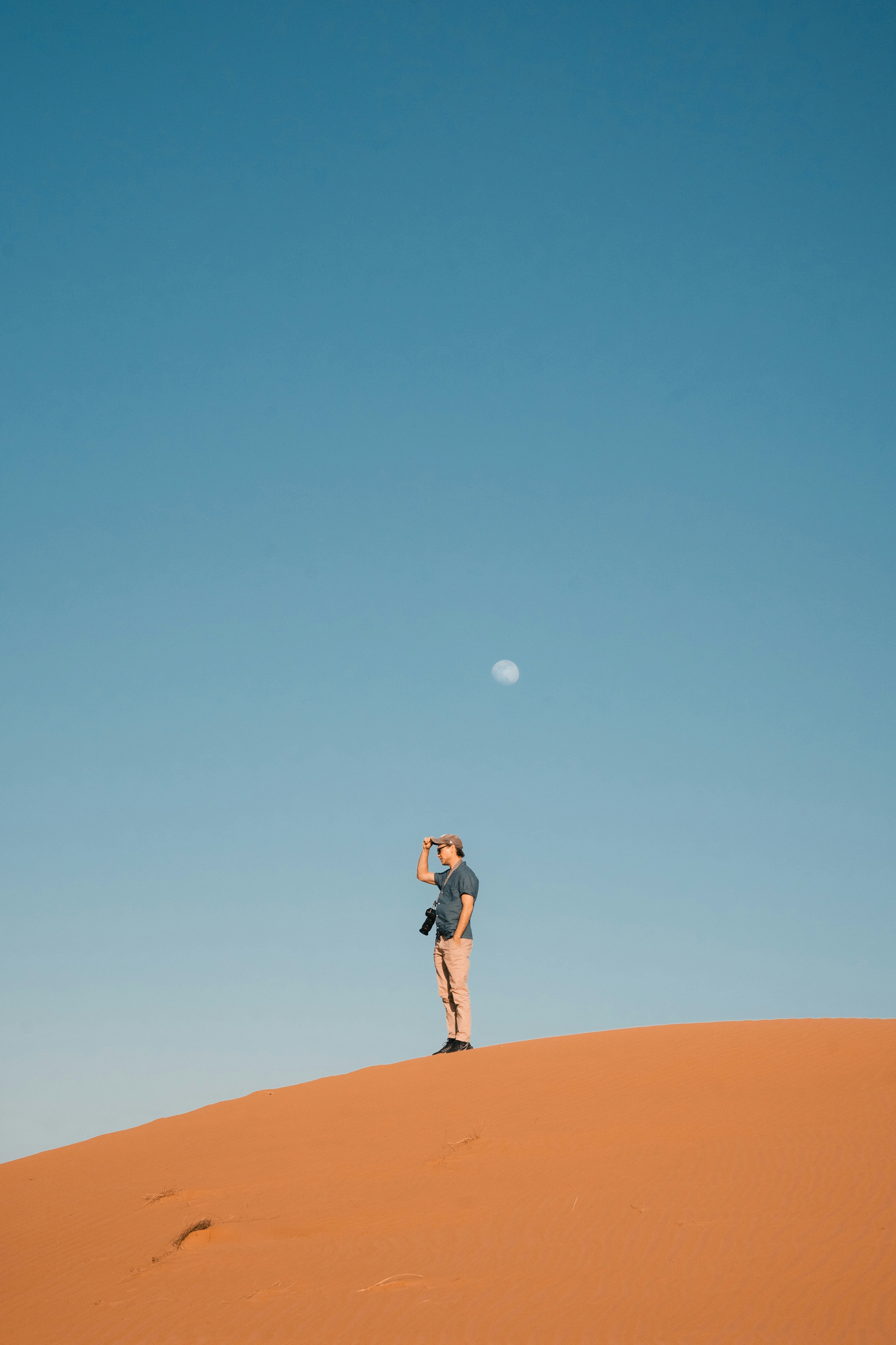 Desert Sentinel: A lone photographer on the wind-sculpted dune under a pale lunar glow