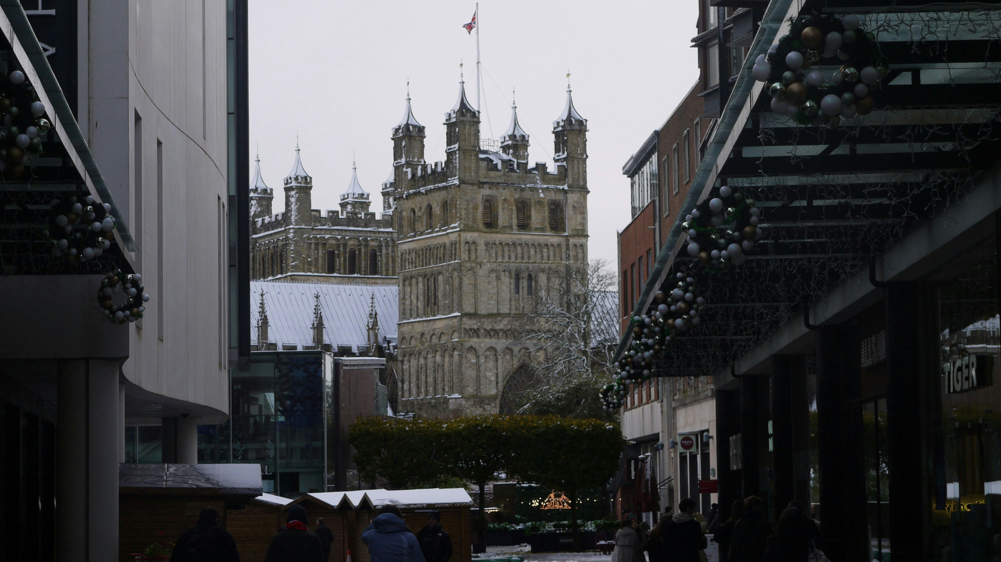 Historic Gothic building framed by contemporary urban architecture under an overcast sky.