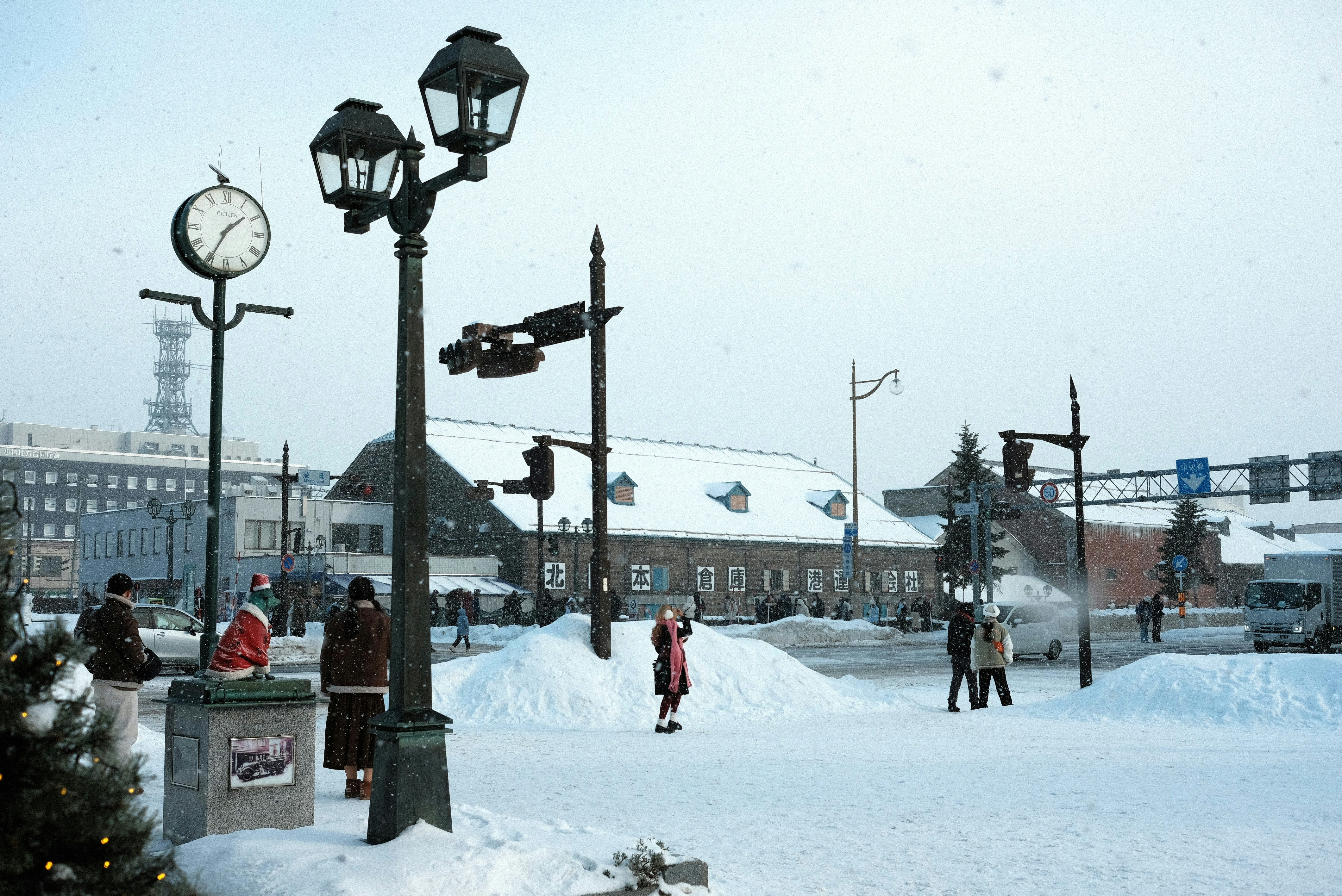 Snow-dusted town square with vintage street lamps and a classic clock set against historic buildings, enveloped in gentle snowfall.