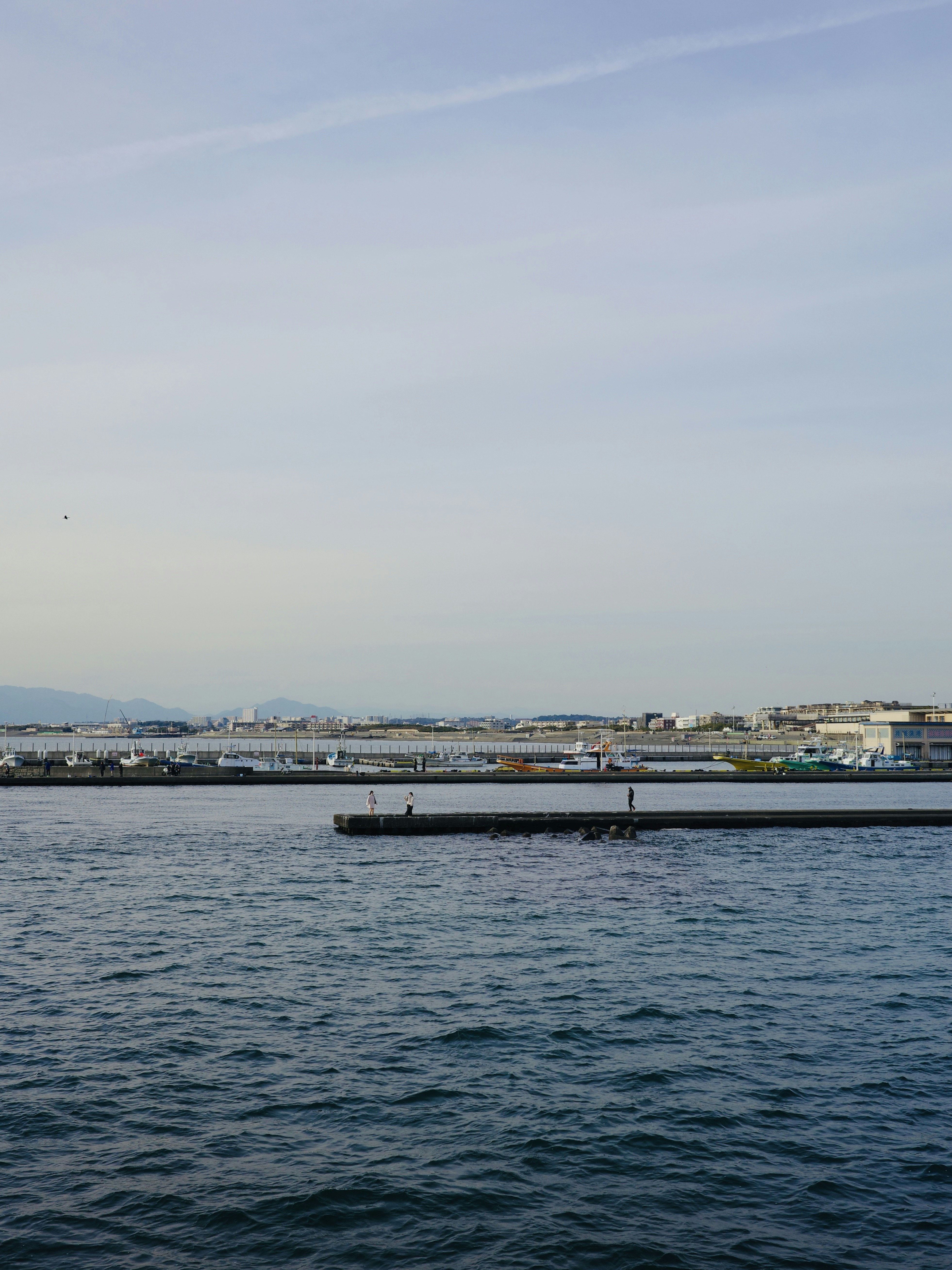 A tranquil harbor scene with a long pier extending into calm waters, framed by distant mountains and a clear sky. The image captures the essence of peaceful coastal life.