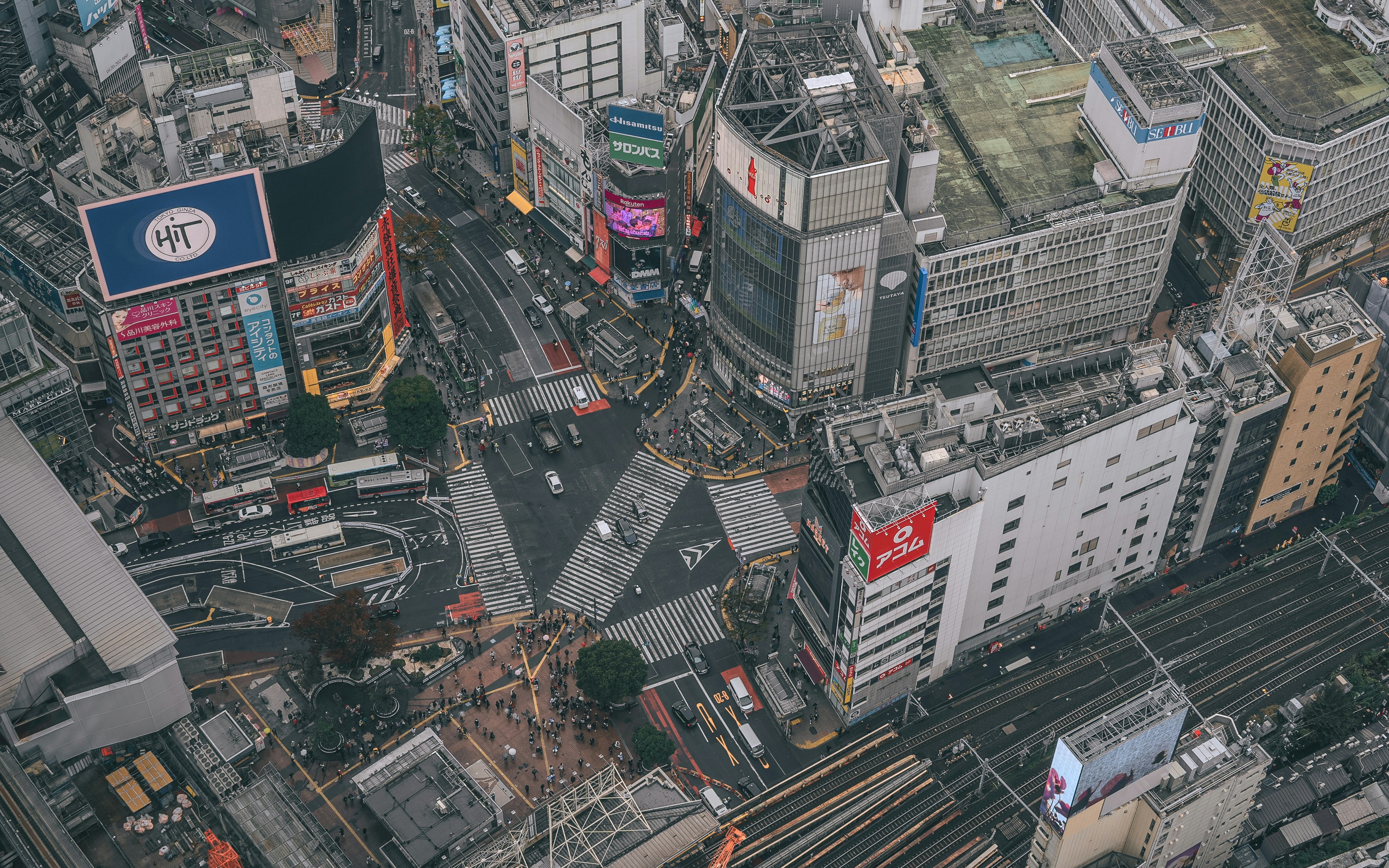 Aerial view of Shibuya's bustling intersection with vibrant advertisements and intricate crosswalks under overcast skies.