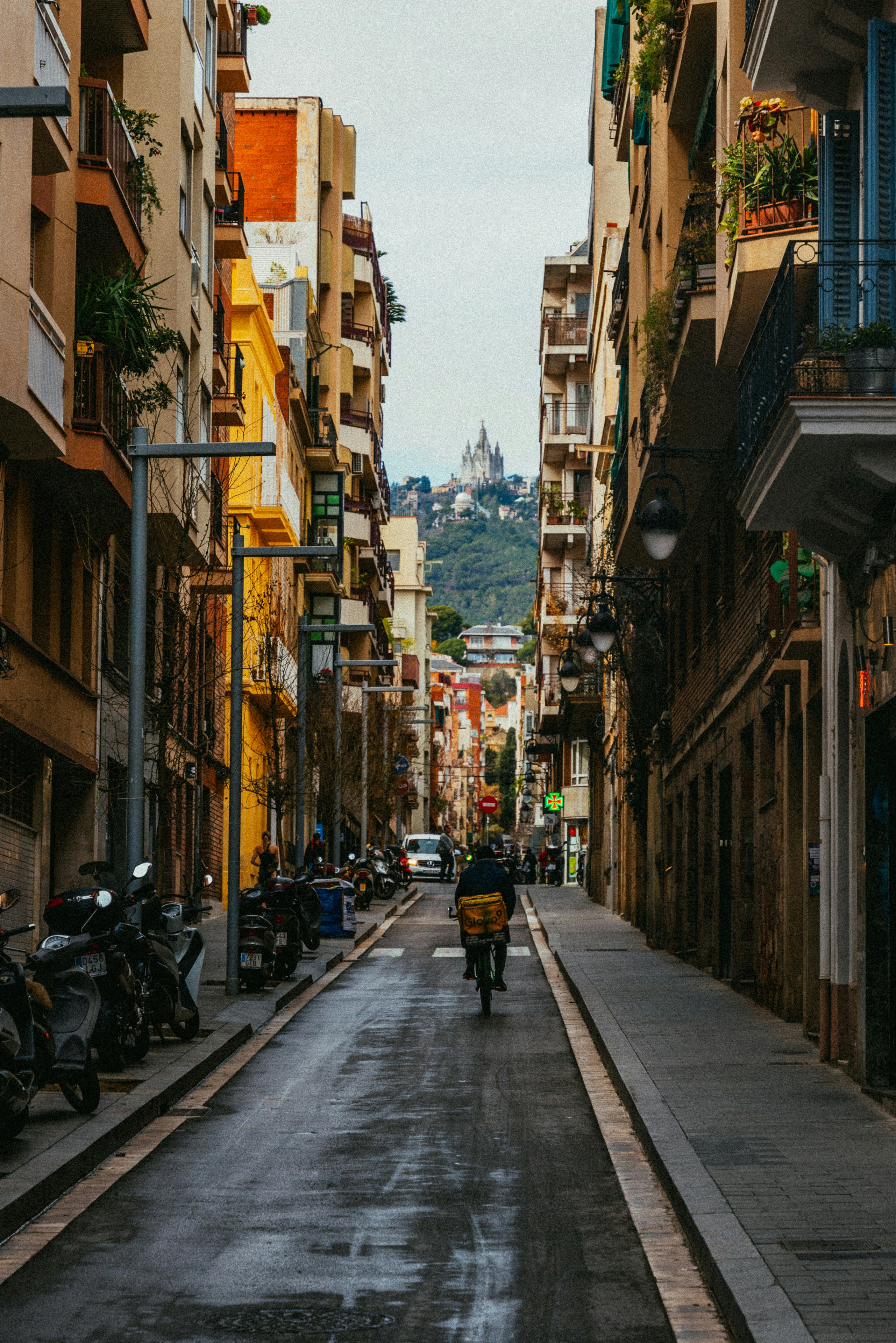 Between Balconies: A Cyclist Carves Through a Rain-Washed Urban Canyon