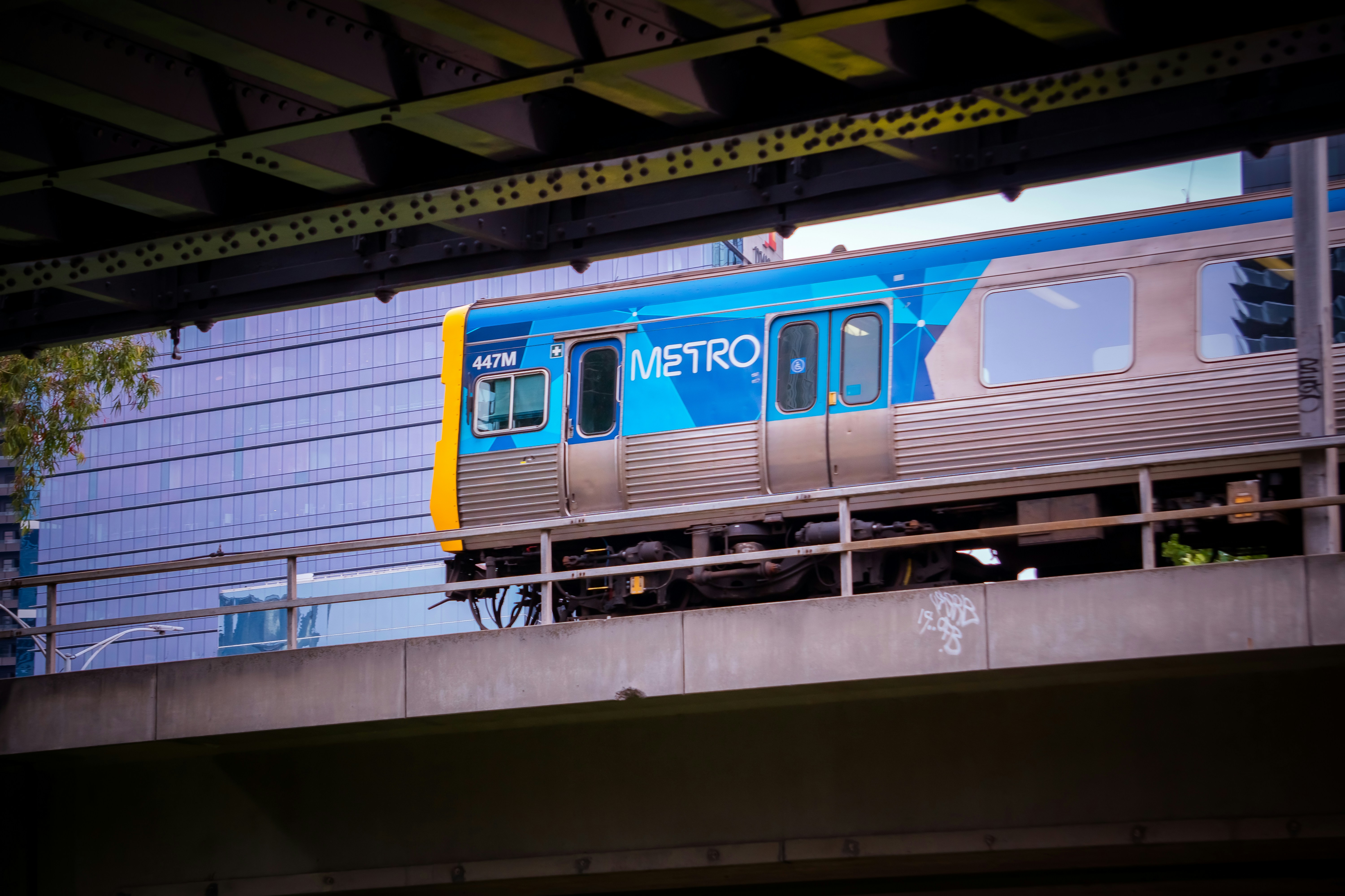 Metro Passages: A blue train glides by beneath a graffiti-free overpass