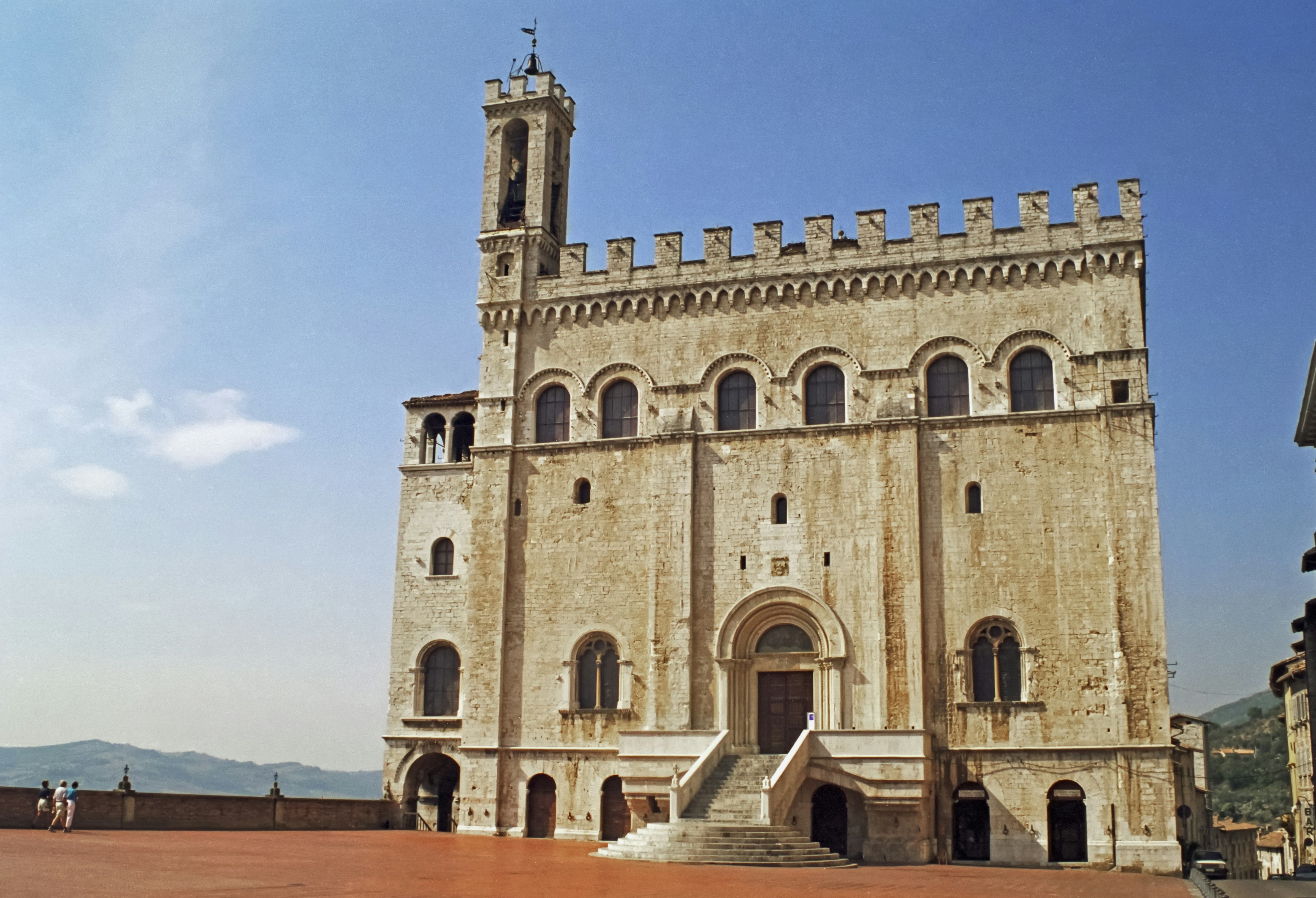 Gothic civic building Palazzo dei Consoli with its symmetrical facade and crenellated parapet under a clear blue sky.
