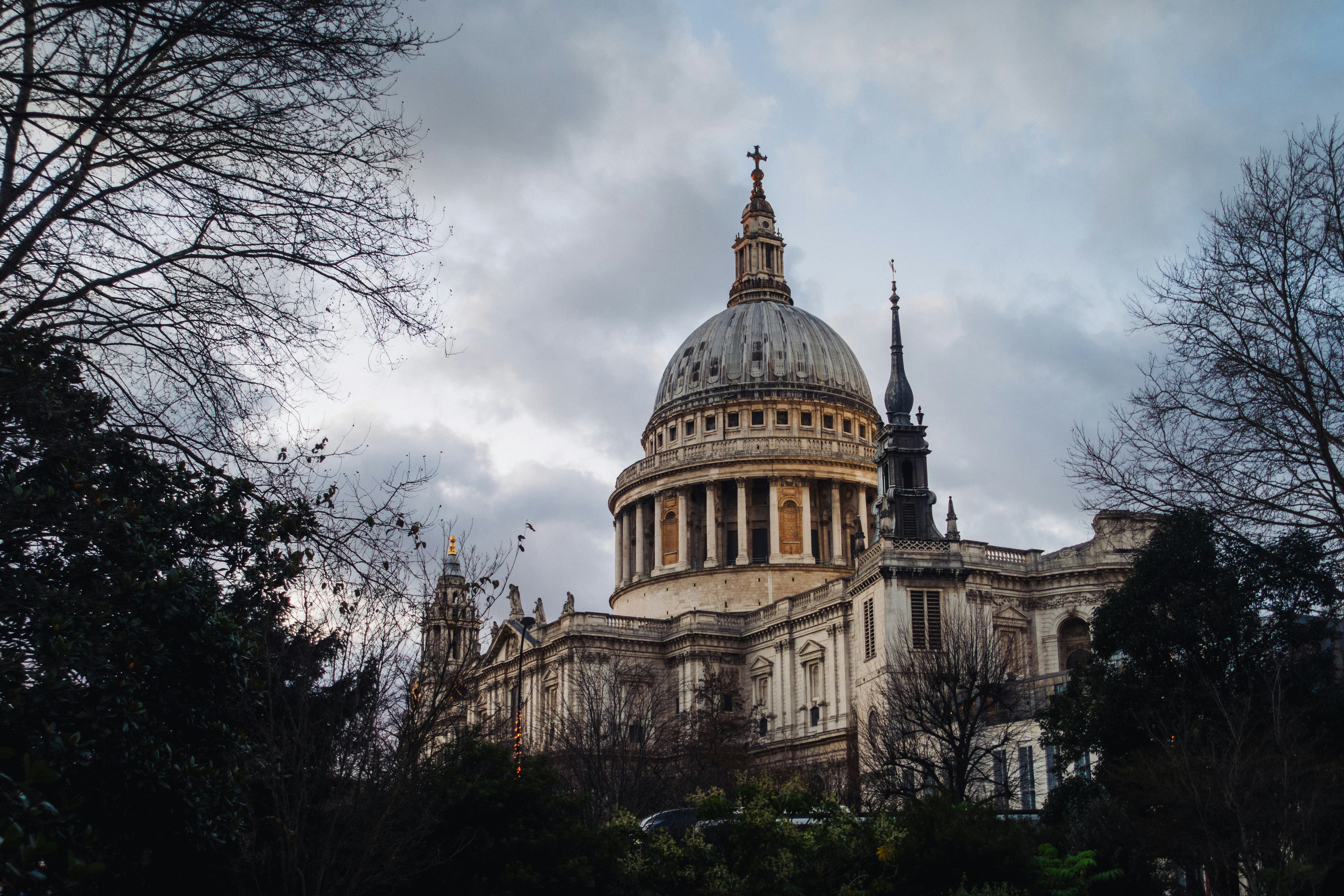 Historic cathedral dome framed by bare winter trees under a dramatic cloudy sky.