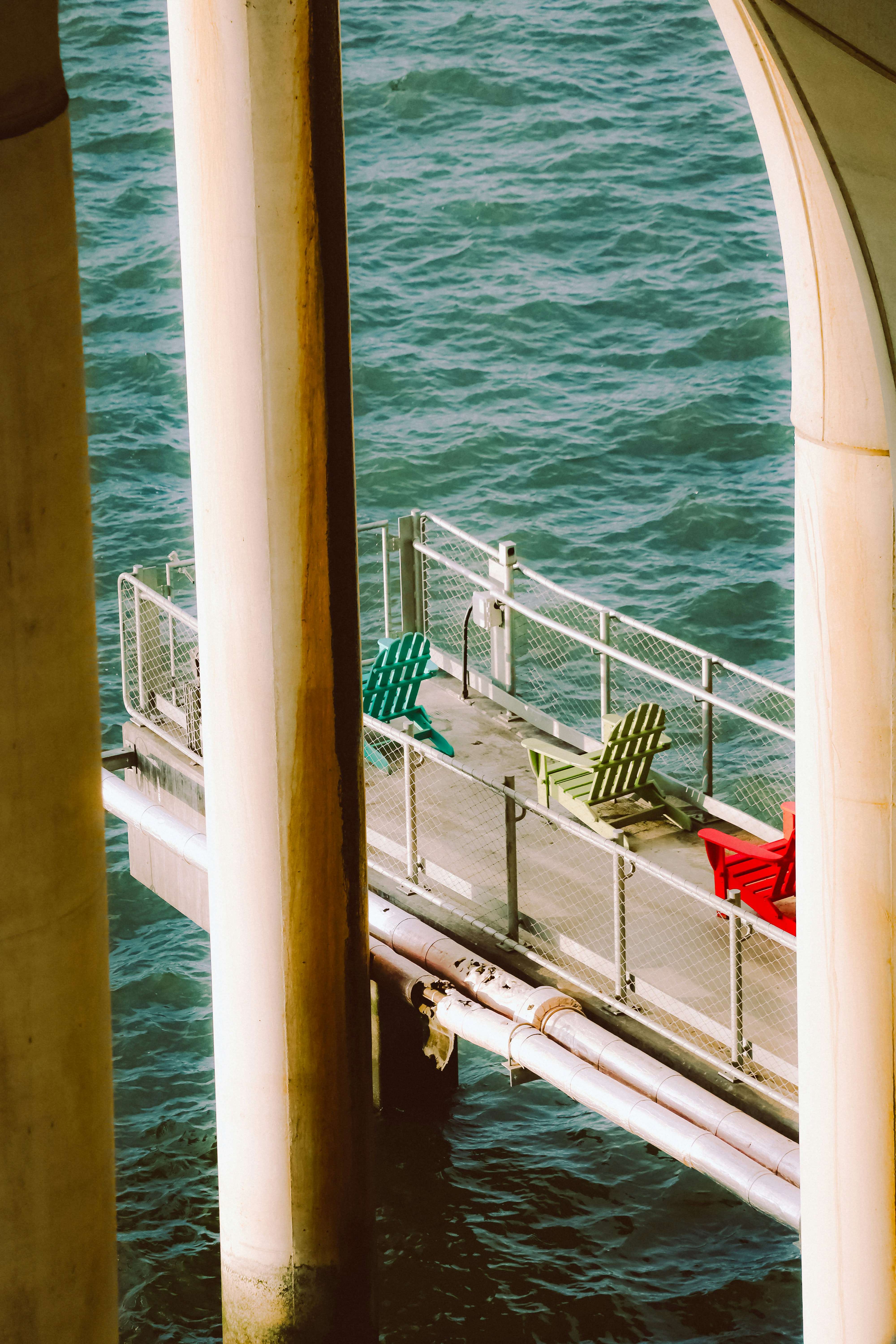 Framed by Pillars: Colorful Adirondack Chairs Over Teal Water