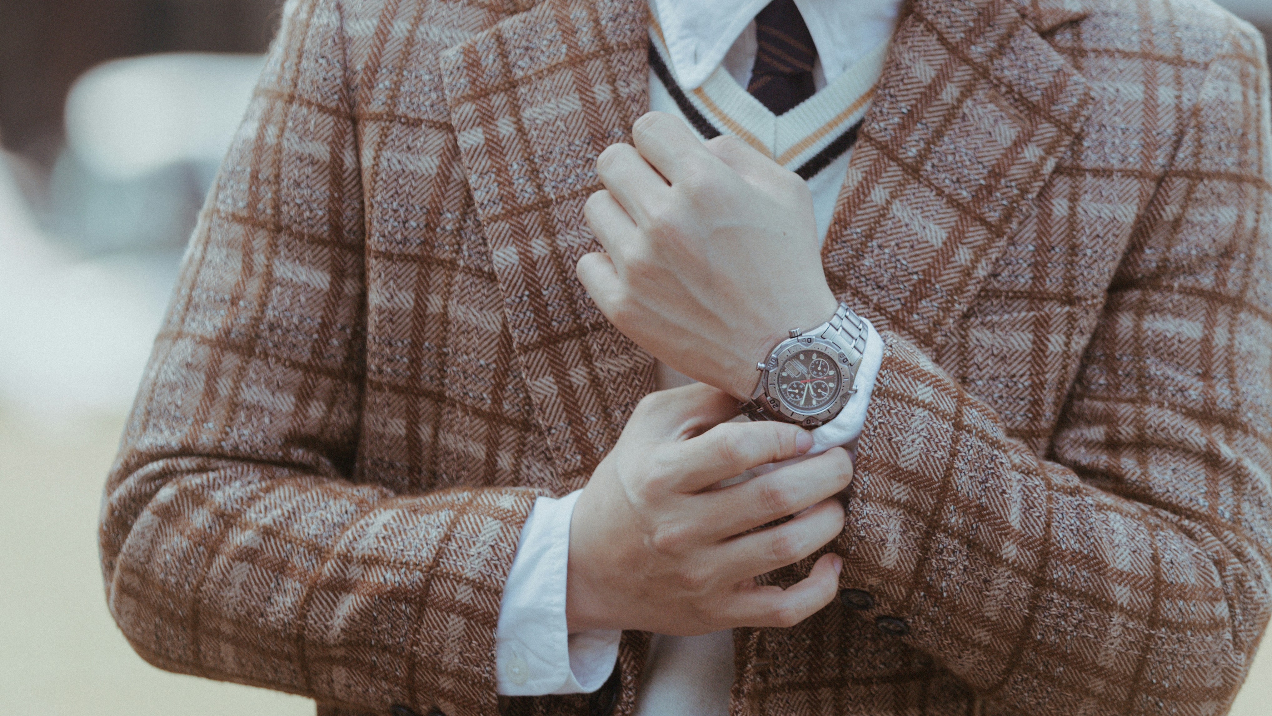 A stylish individual adjusts a classic watch while wearing a sophisticated plaid blazer, embodying a blend of fashion and functionality.