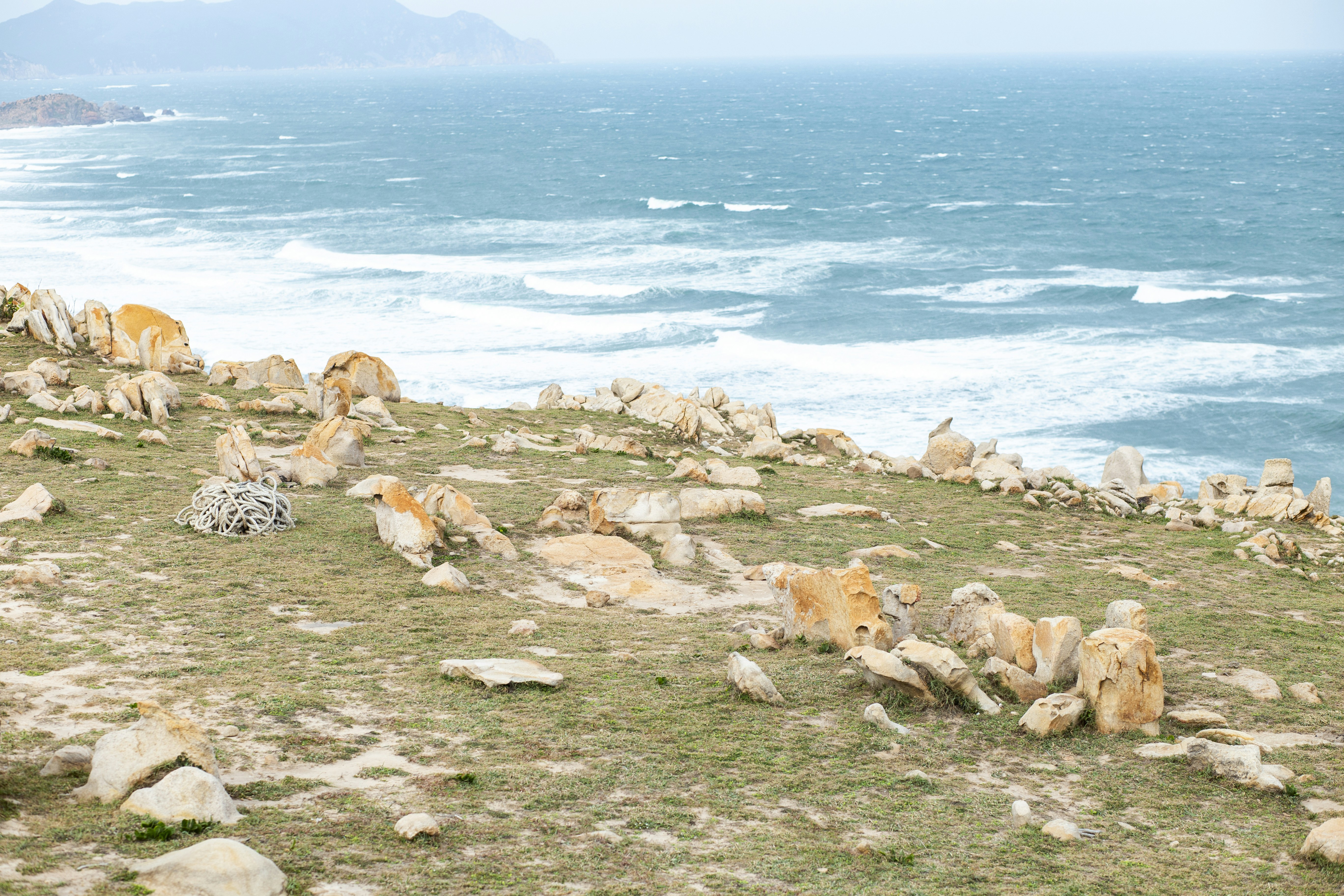 Rocky coastline meets turquoise waves under a soft, expansive sky.