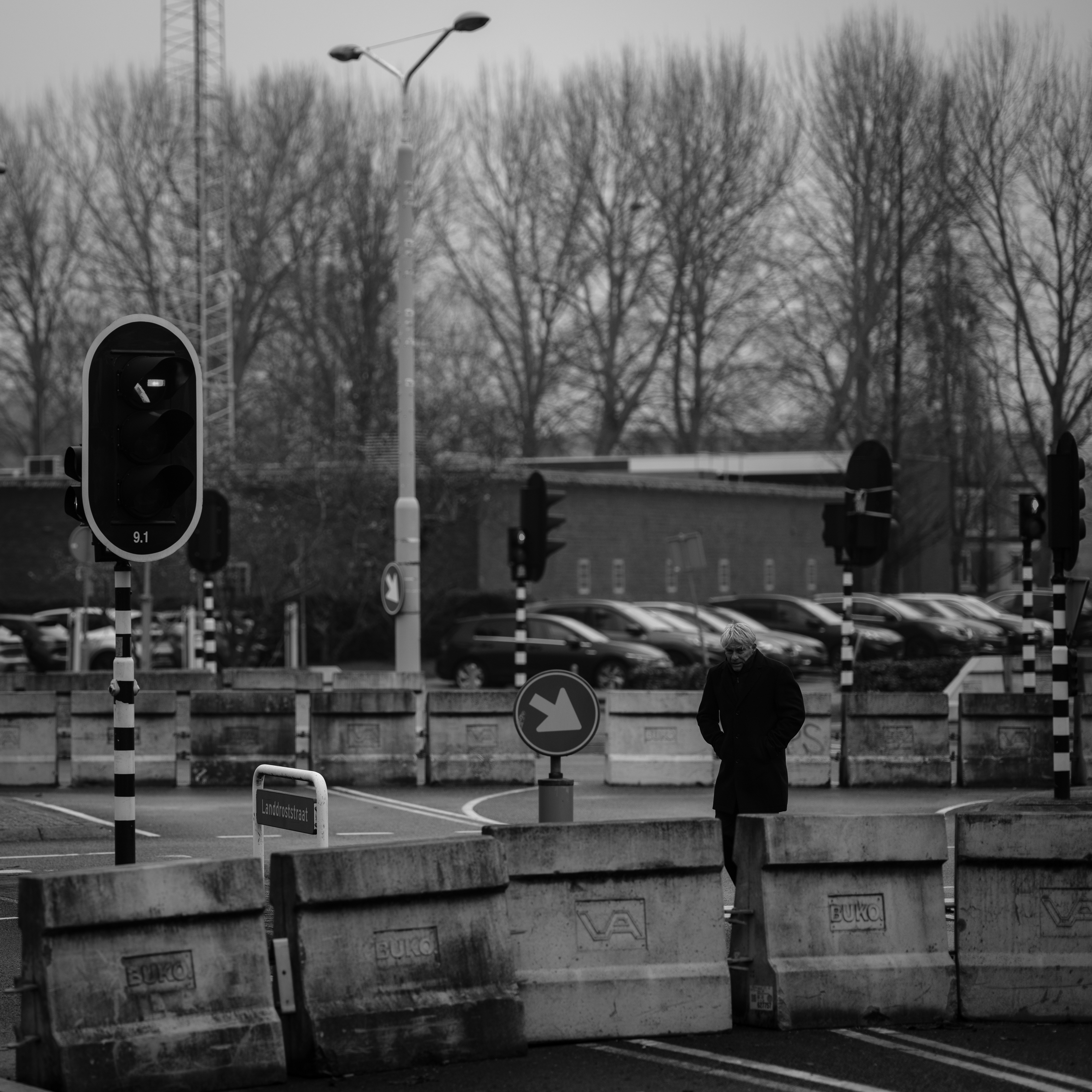 Edge of the Barrier: A Solitary Figure Anchors a Monochrome Street Scene
