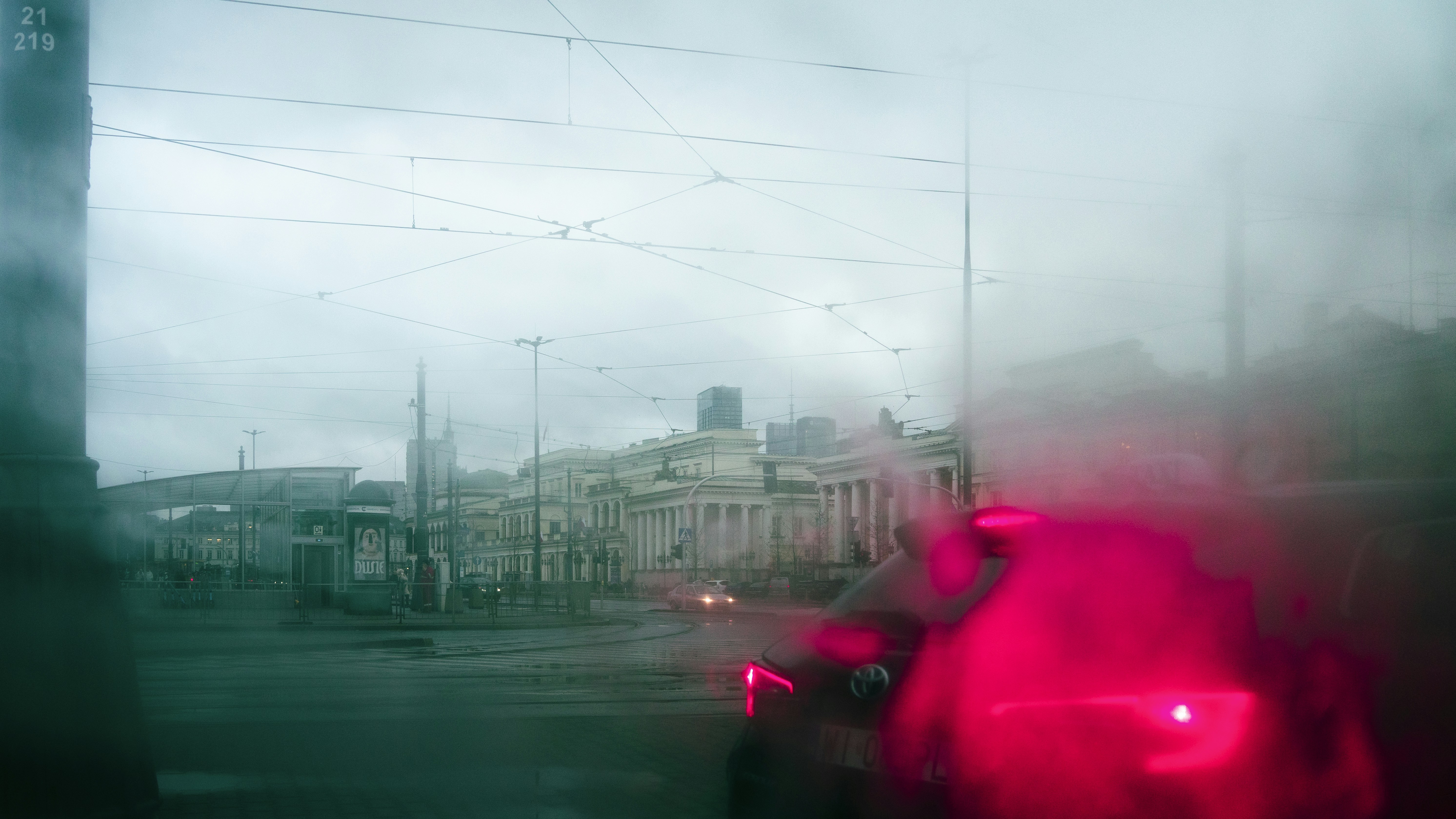 Cityscape through a foggy window with blurred car lights and historic buildings in the background.