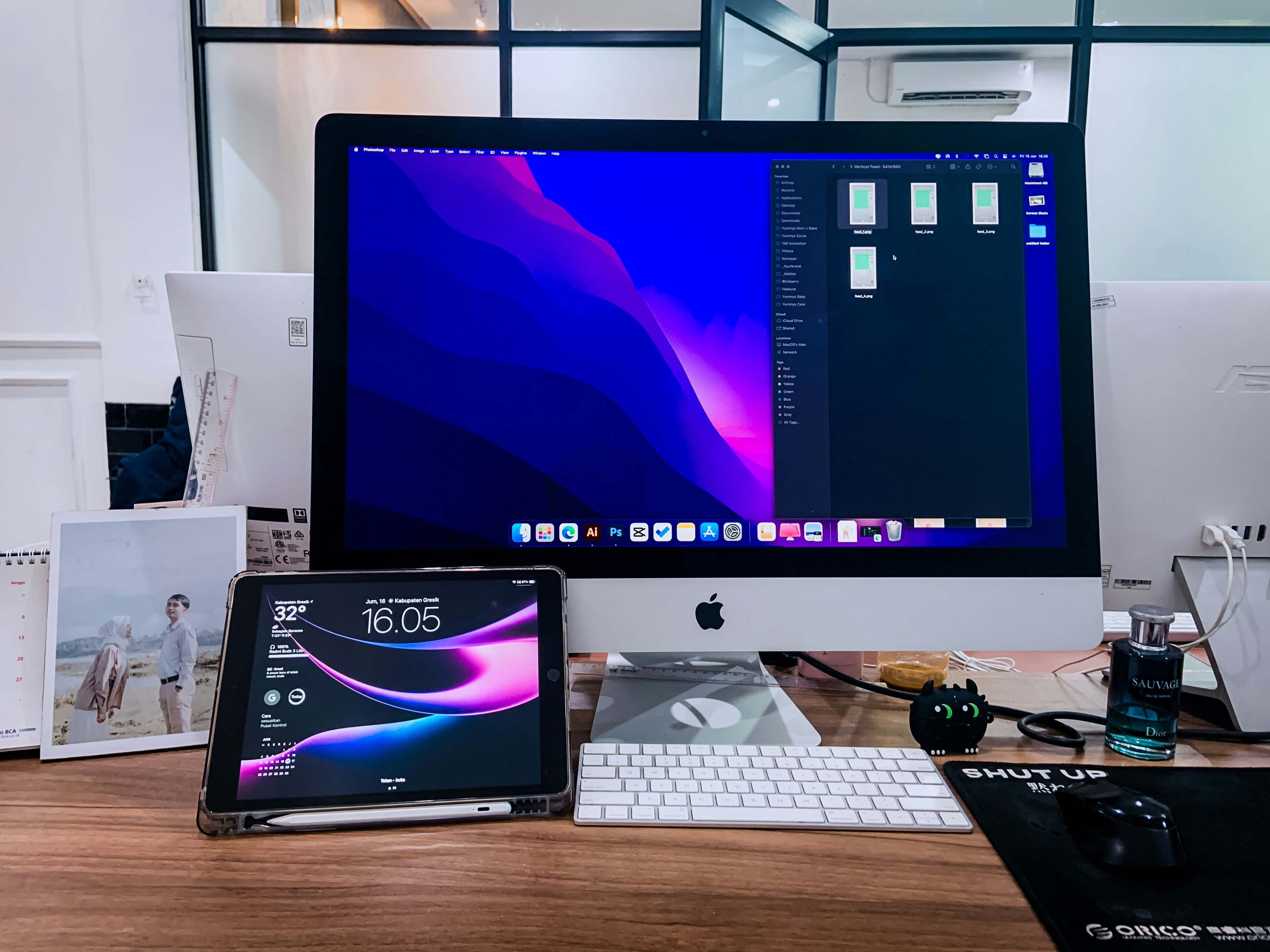 Sleek workspace featuring an Apple iMac and iPad, surrounded by personal touches like a calendar and a mouse pad. The vibrant screens showcase a digital interface.