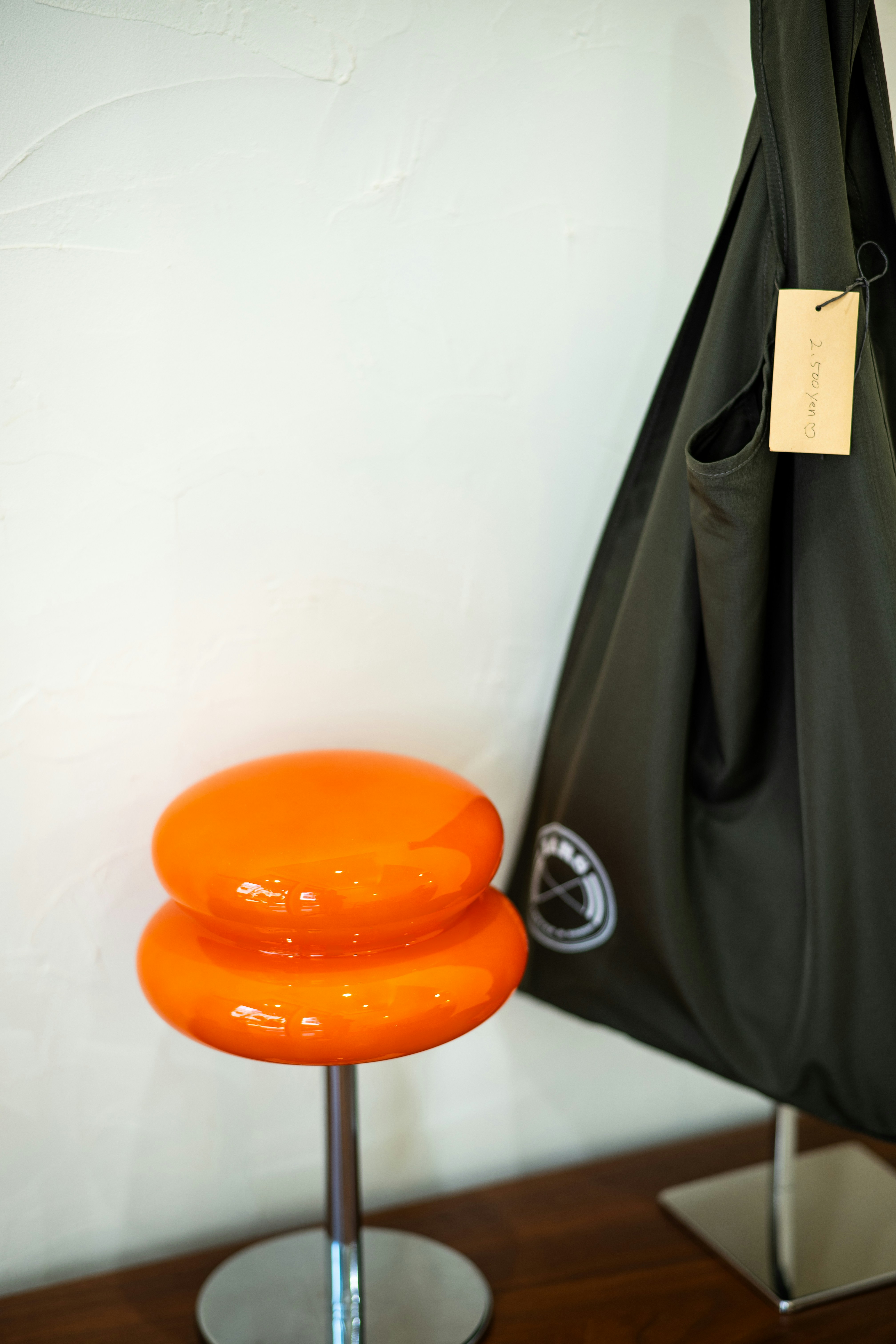 Glossy Orange Stool in a Minimal Studio Corner with a Draped Coat