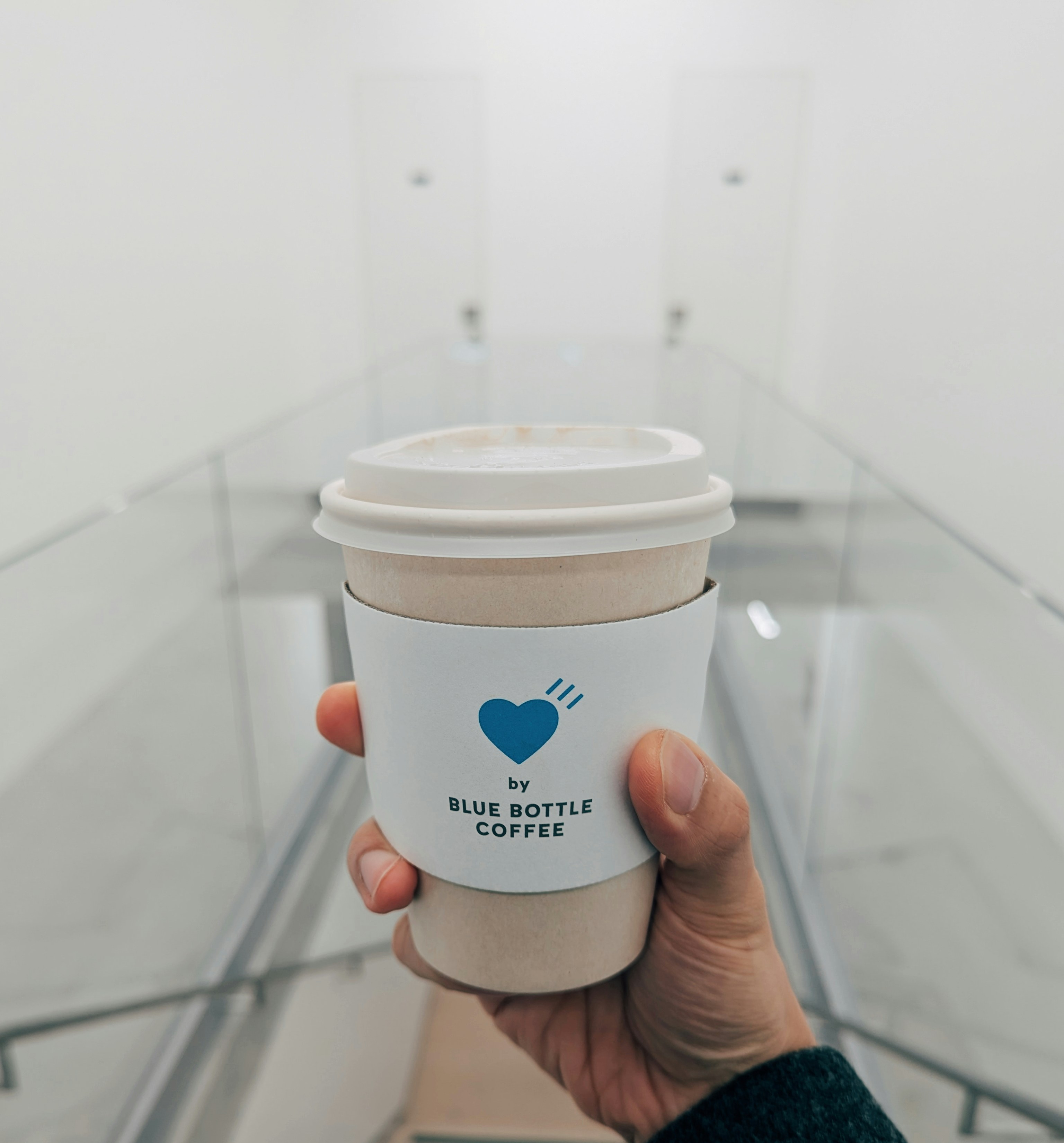 Blue Bottle Moment: Hand-Held Cup in a Minimal Glass Corridor