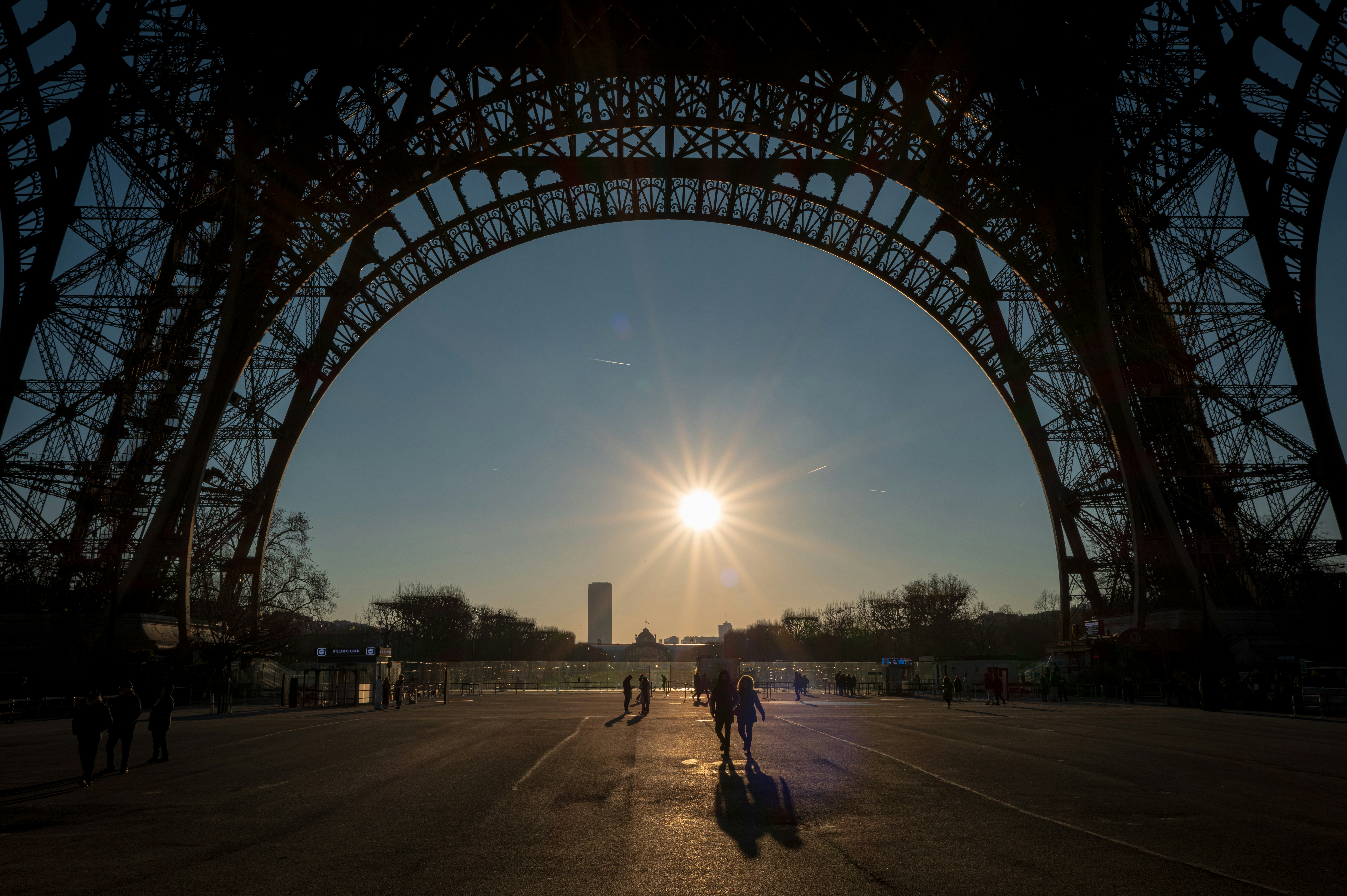 Sunlit Archway: People Walking Toward the Light Under a Shadowed Iron Frame