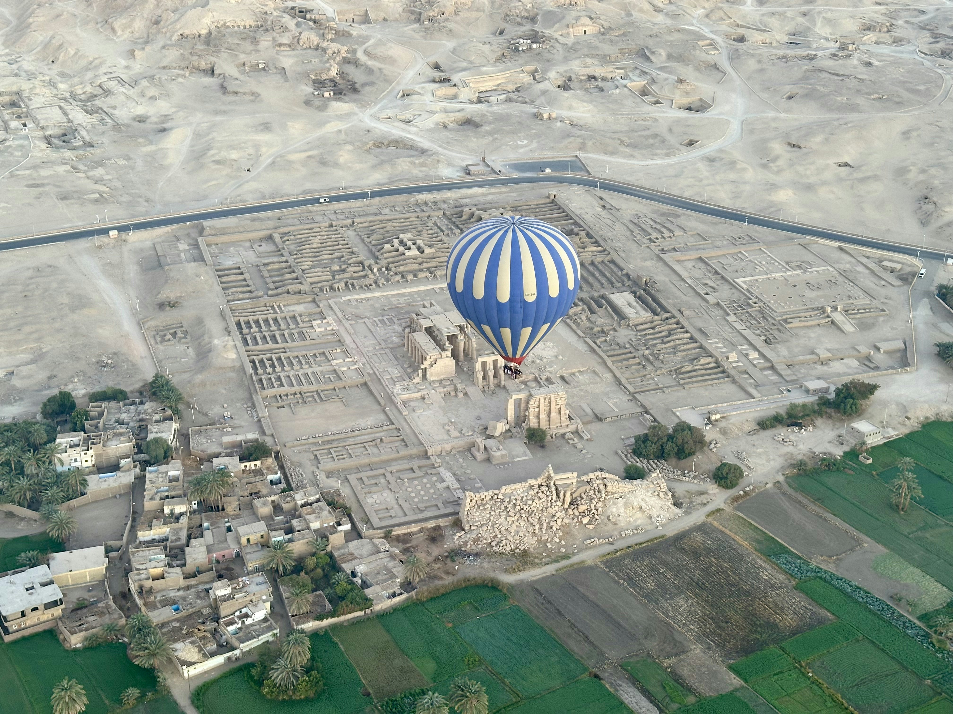 Hot air balloon floating above desert ruins and green fields.