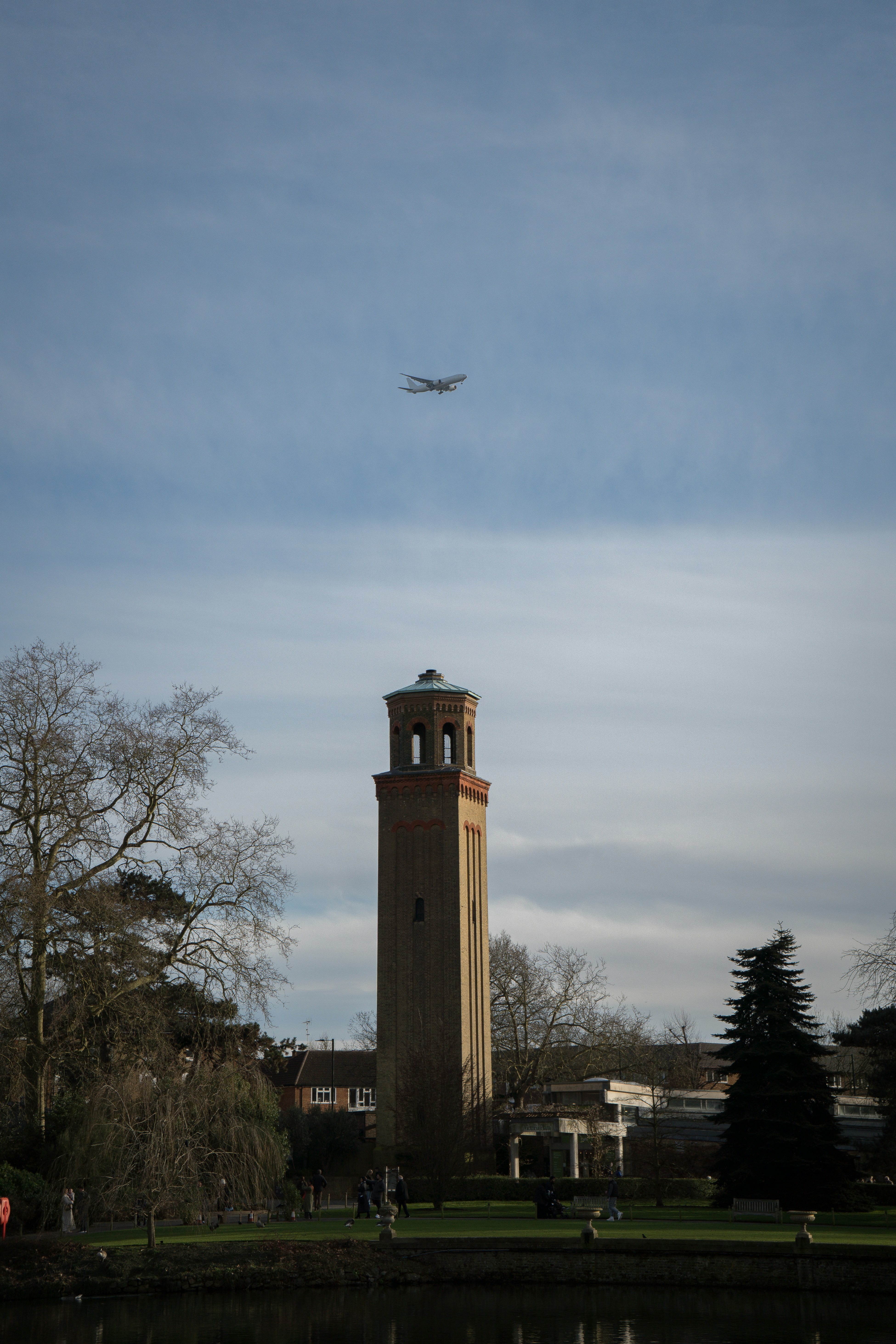 Plane Crossing Above a Brick Clock Tower in a Tranquil Park