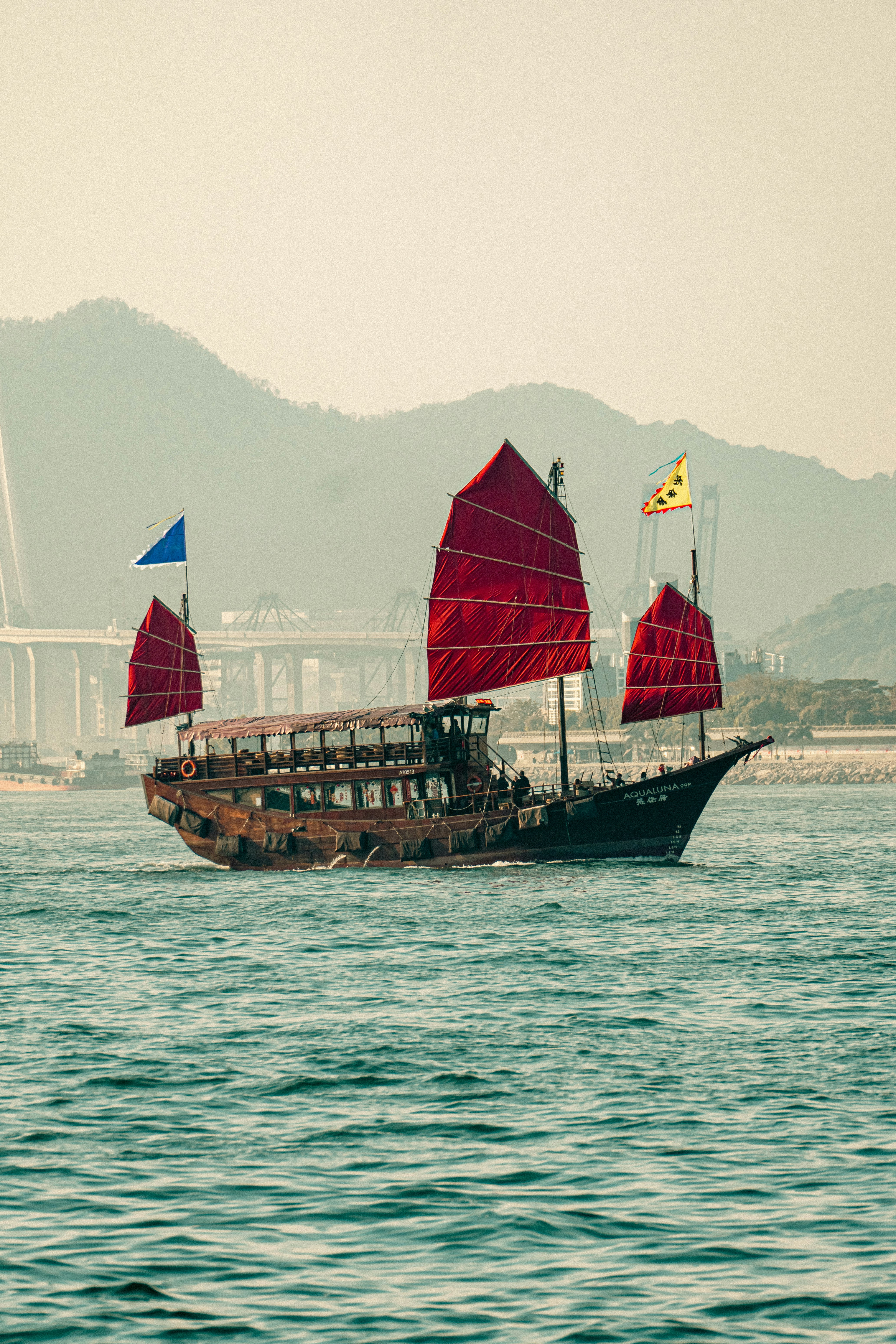 Crimson Junk Drifts Through a Quiet Harbor Under Misty Hills