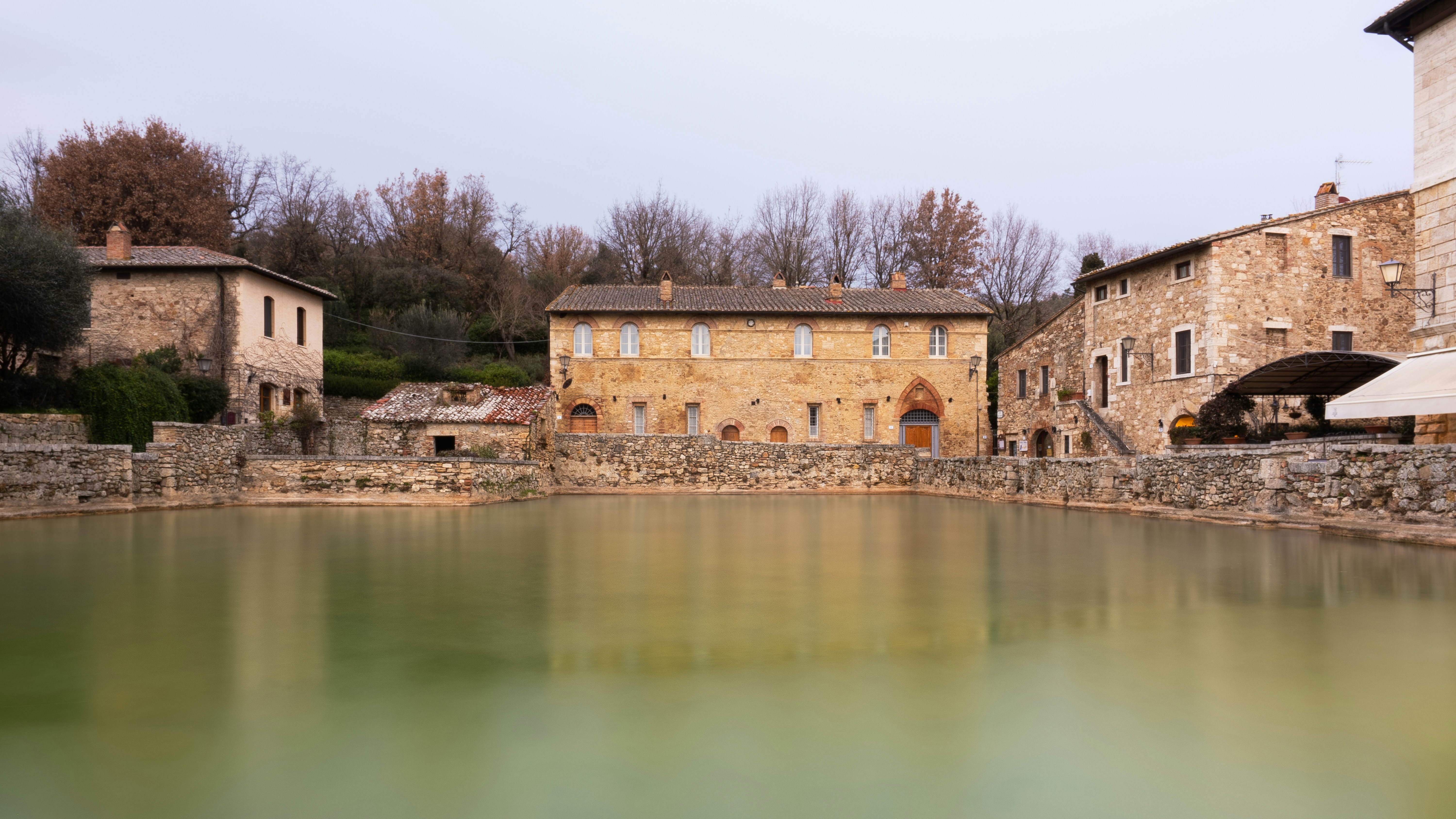 Historic stone buildings surround a tranquil thermal pool in Bagno Vignoni, Tuscany.